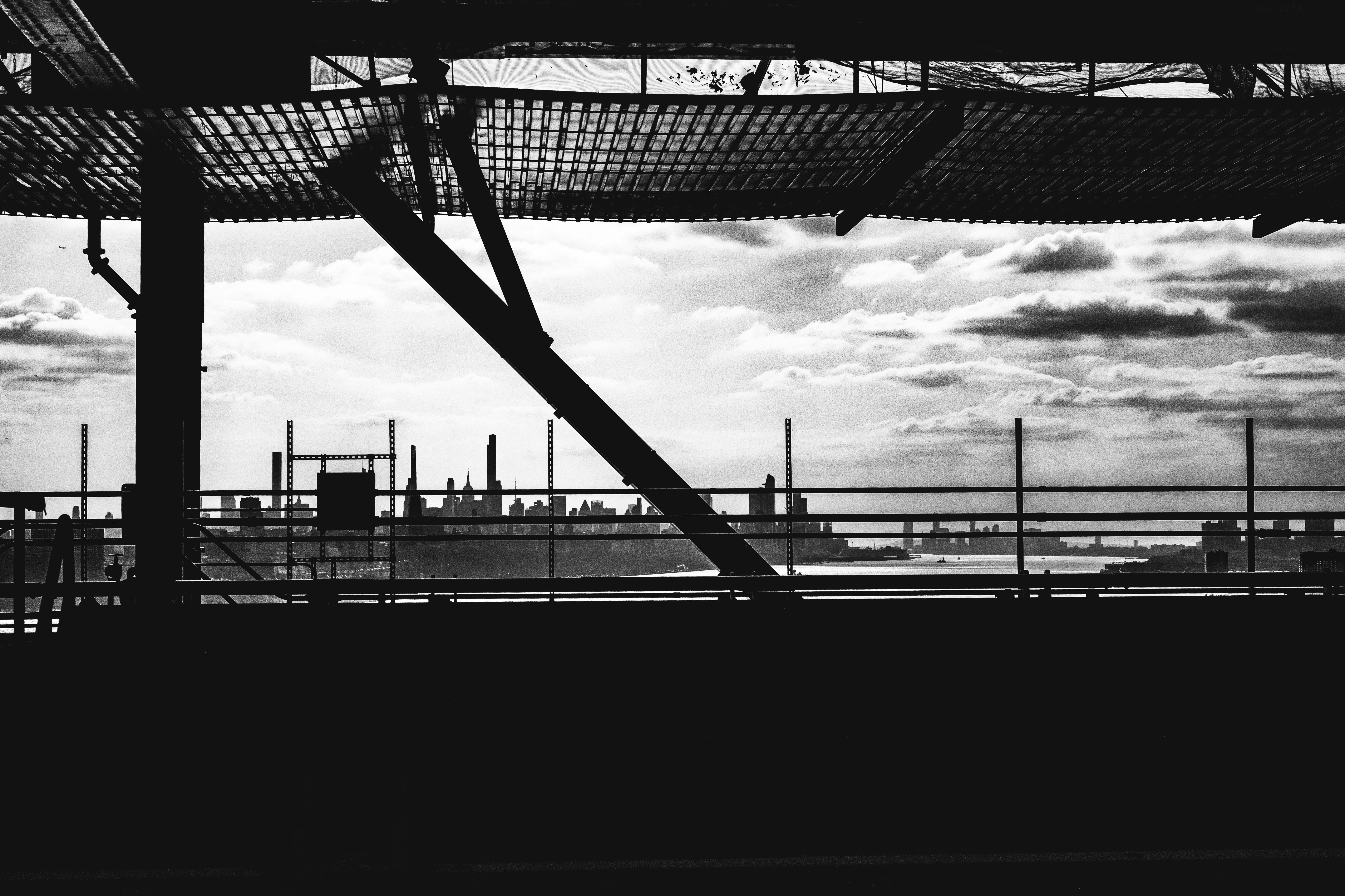 Silhouette of industrial structures against a cloudy skyline, framed by architectural elements. The stark contrast emphasizes the urban landscape's complexity.