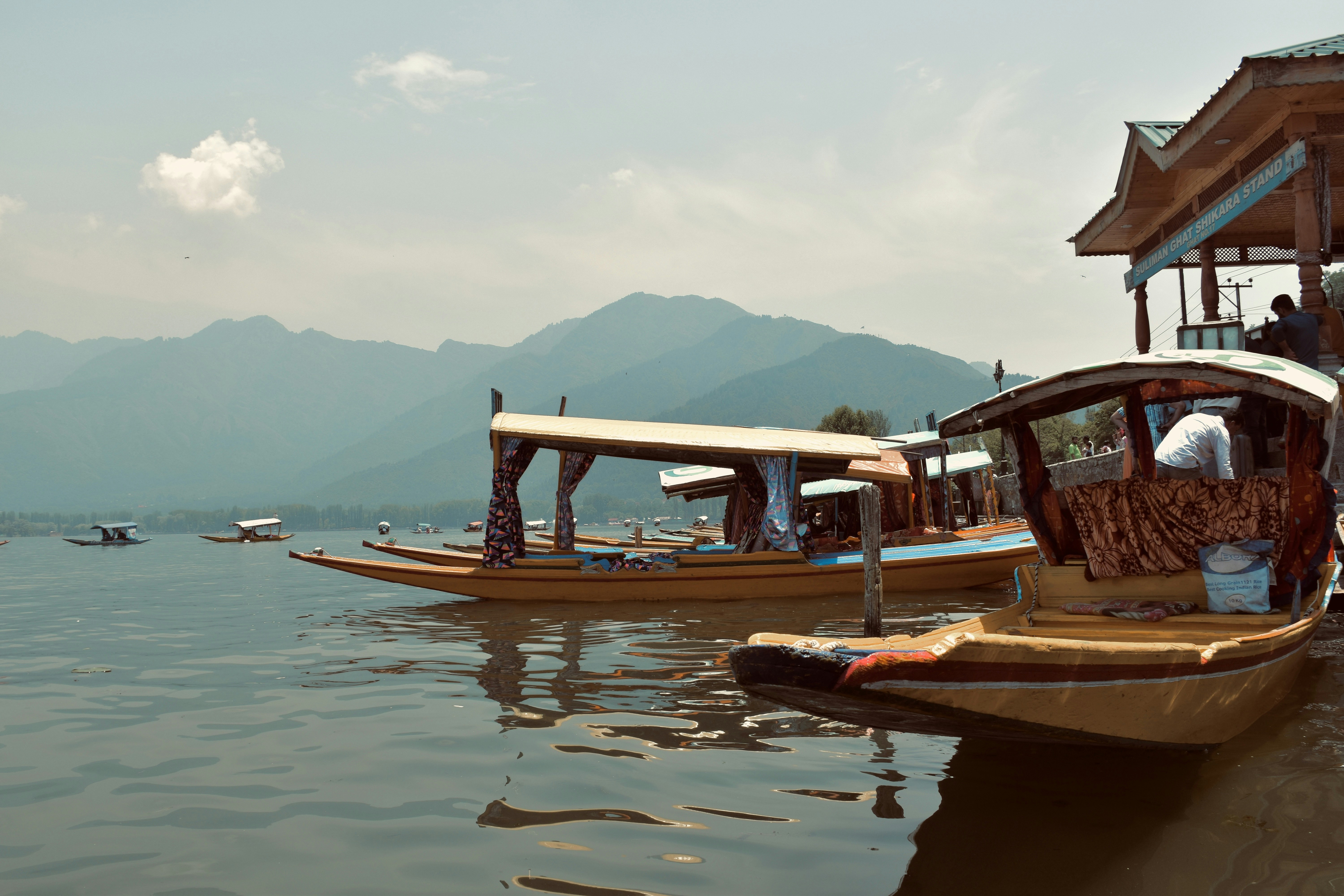 Wooden boats moored on Dal Lake with misty mountains in the background under a partly cloudy sky.