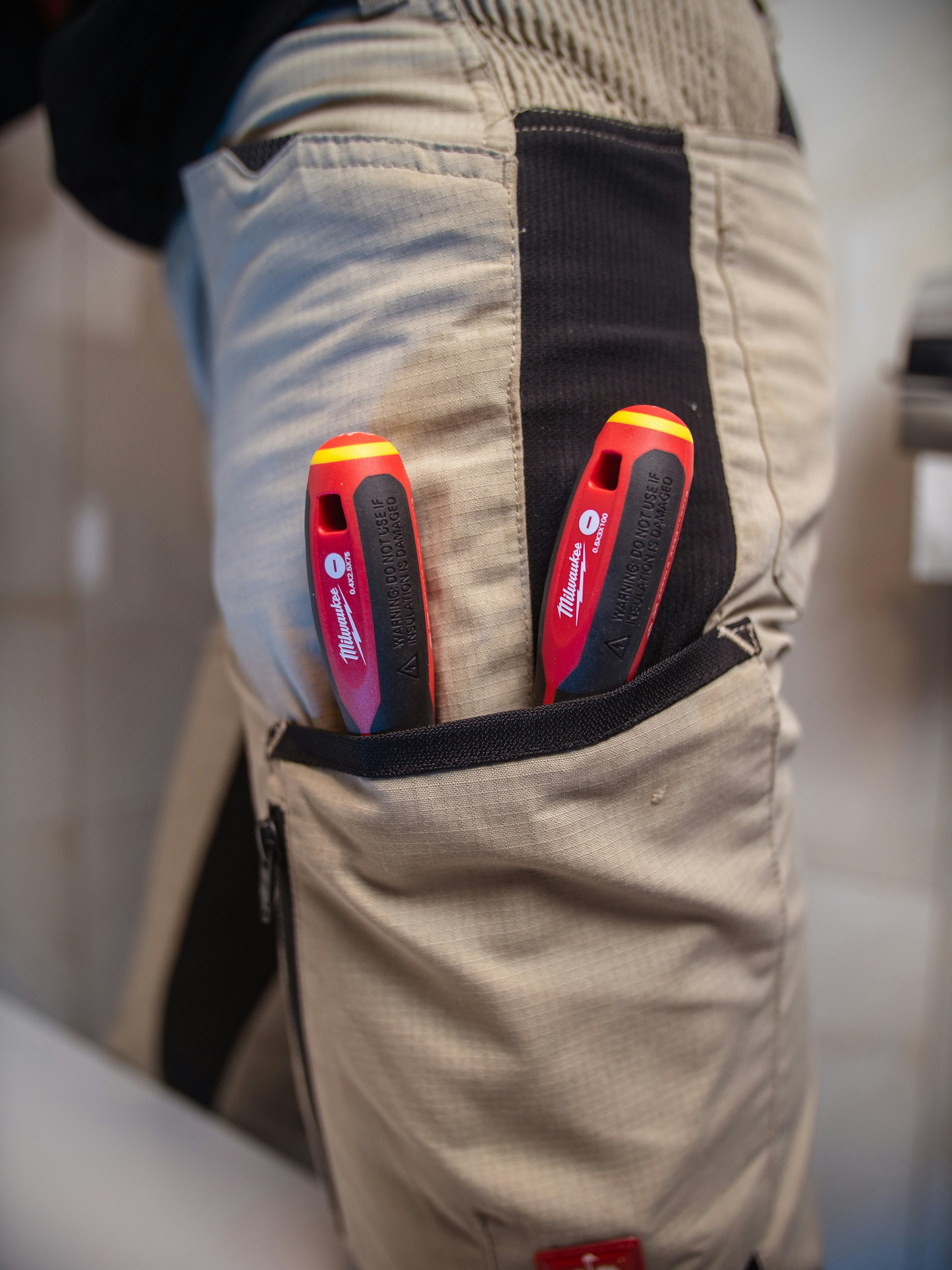 Tool Belt Essentials: Red and Yellow Utility Pliers Rest in a Beige Work Pant Pocket