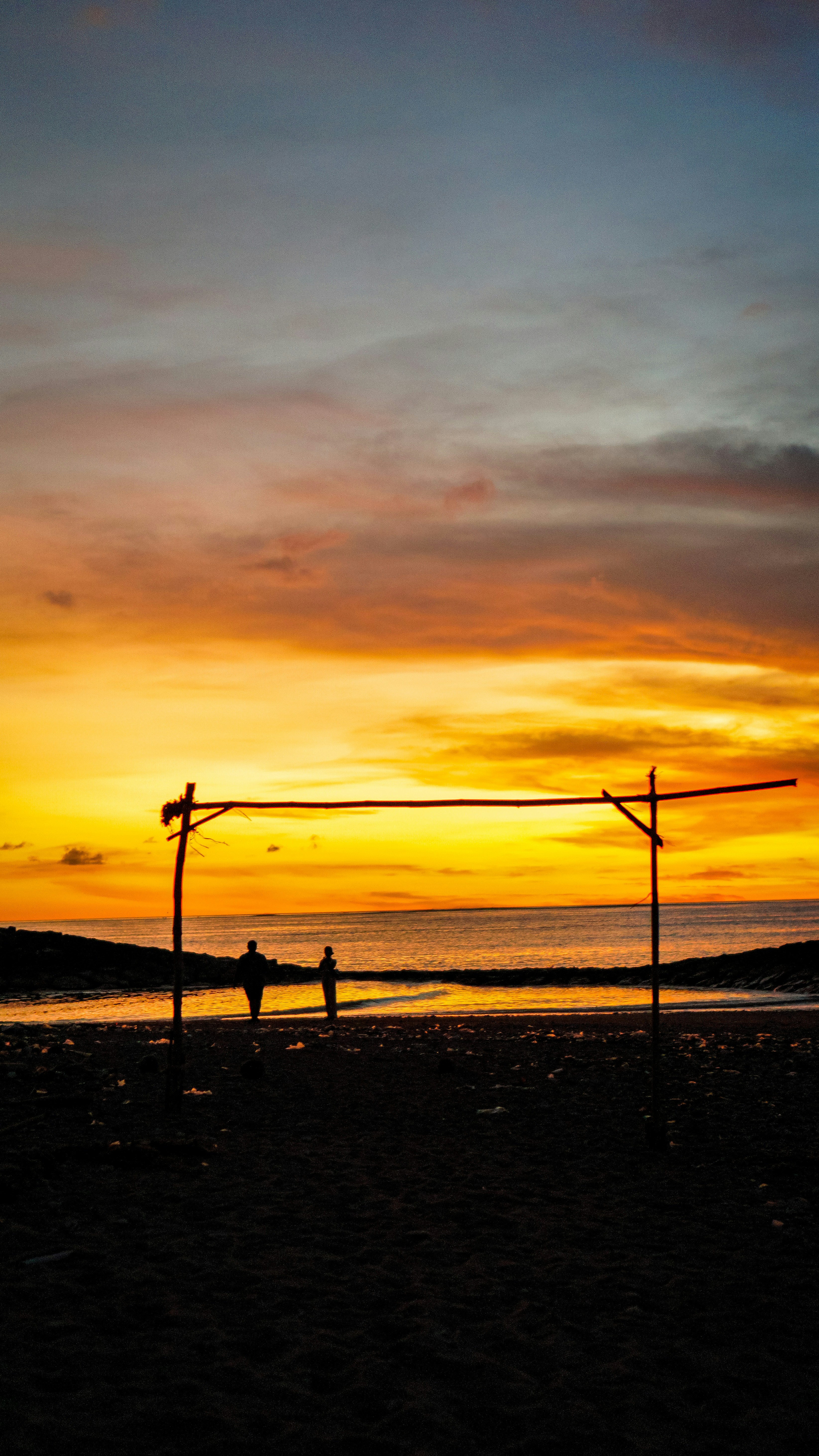 Silhouette at Sunset: Two Figures Under a Simple Gate on the Shore