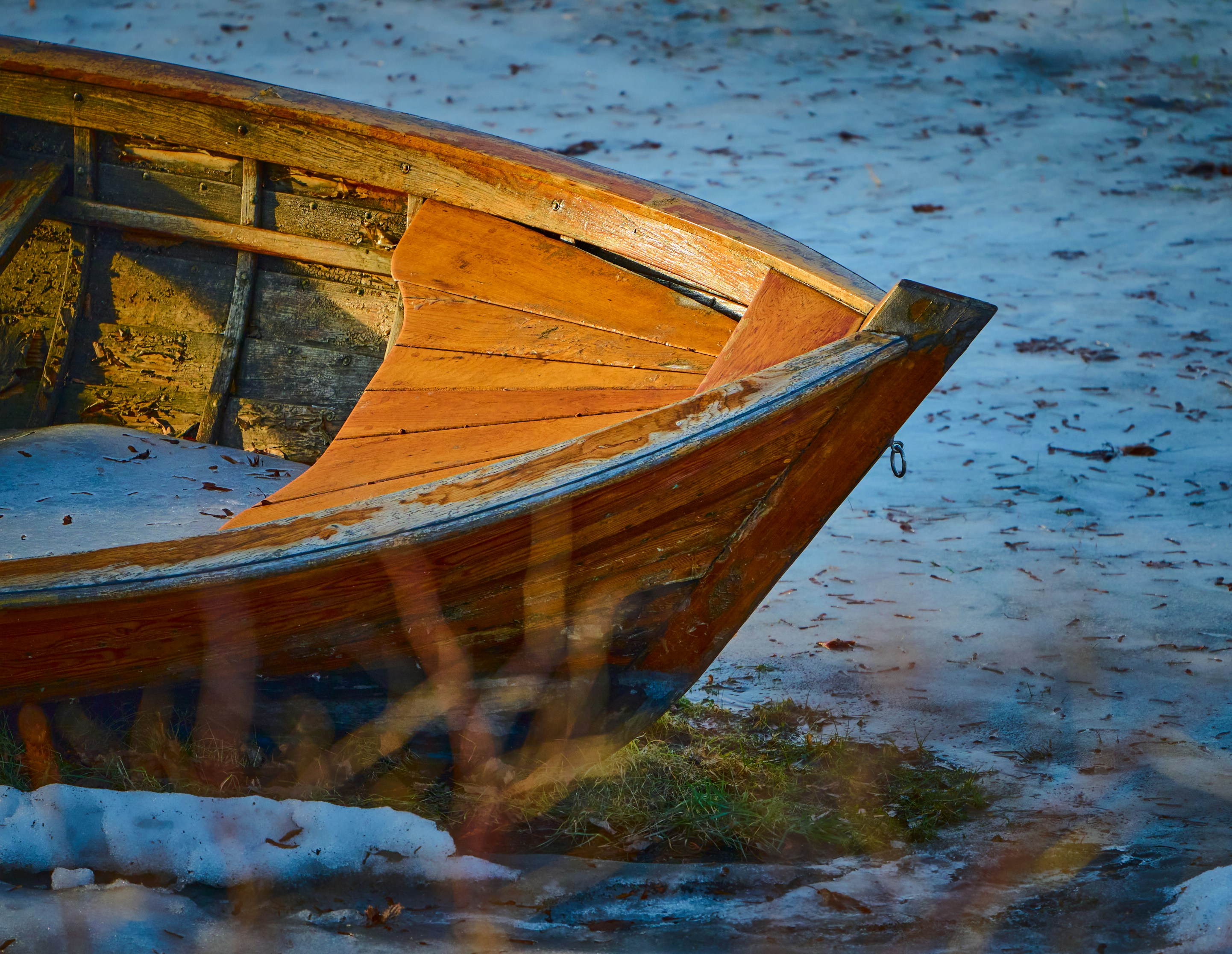 A close-up of a wooden boat resting on the snow, showcasing its intricate craftsmanship and natural aging. The scene captures the serene intersection of wood and winter.
