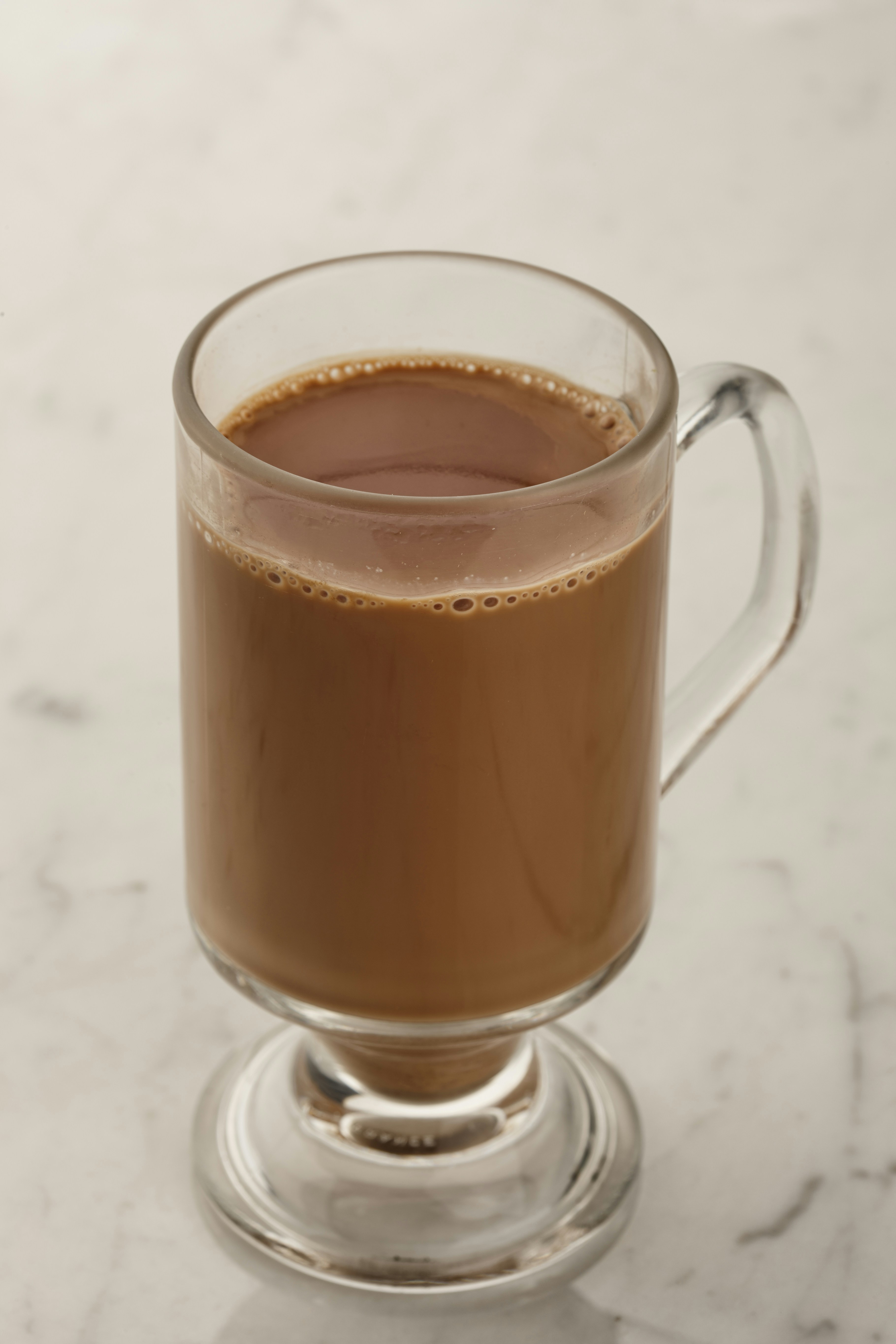 Glass mug filled with rich brown beverage resting on a marble surface.