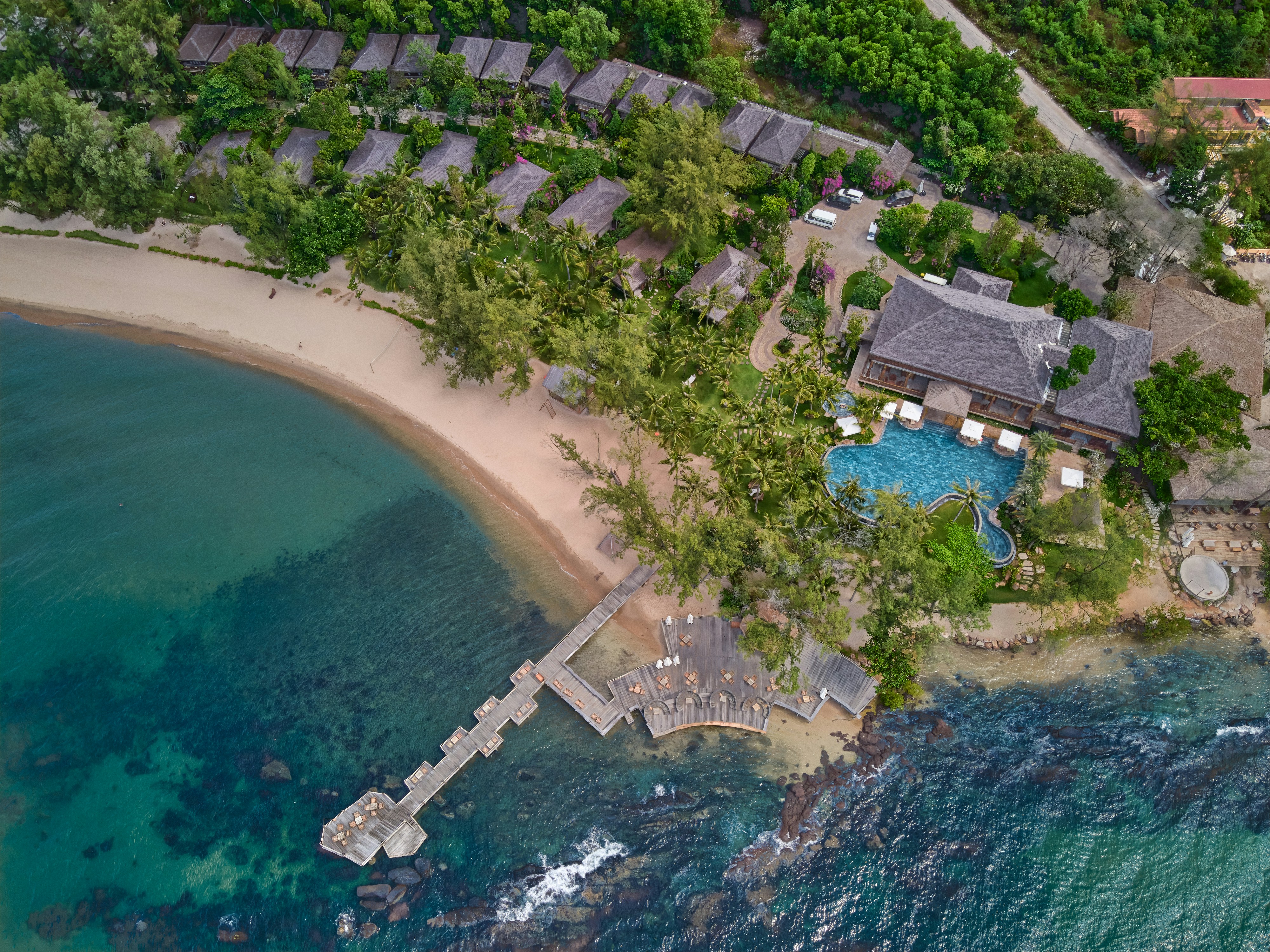 Aerial view of a lush resort with a beachfront and dock extending into the ocean.