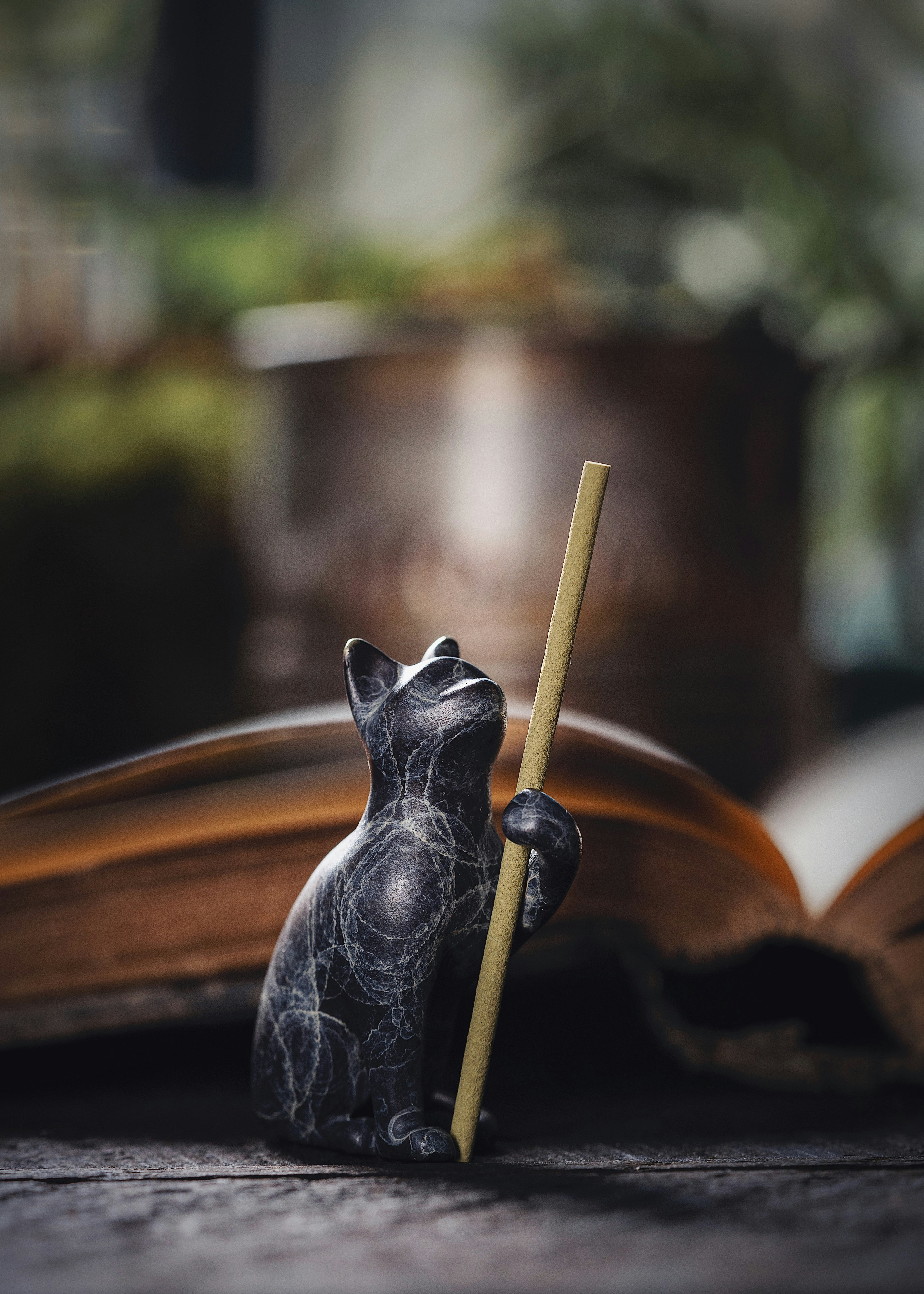 Whiskers at the Desk: A Marble-Furred Cat Clutches a Reed by Open Pages