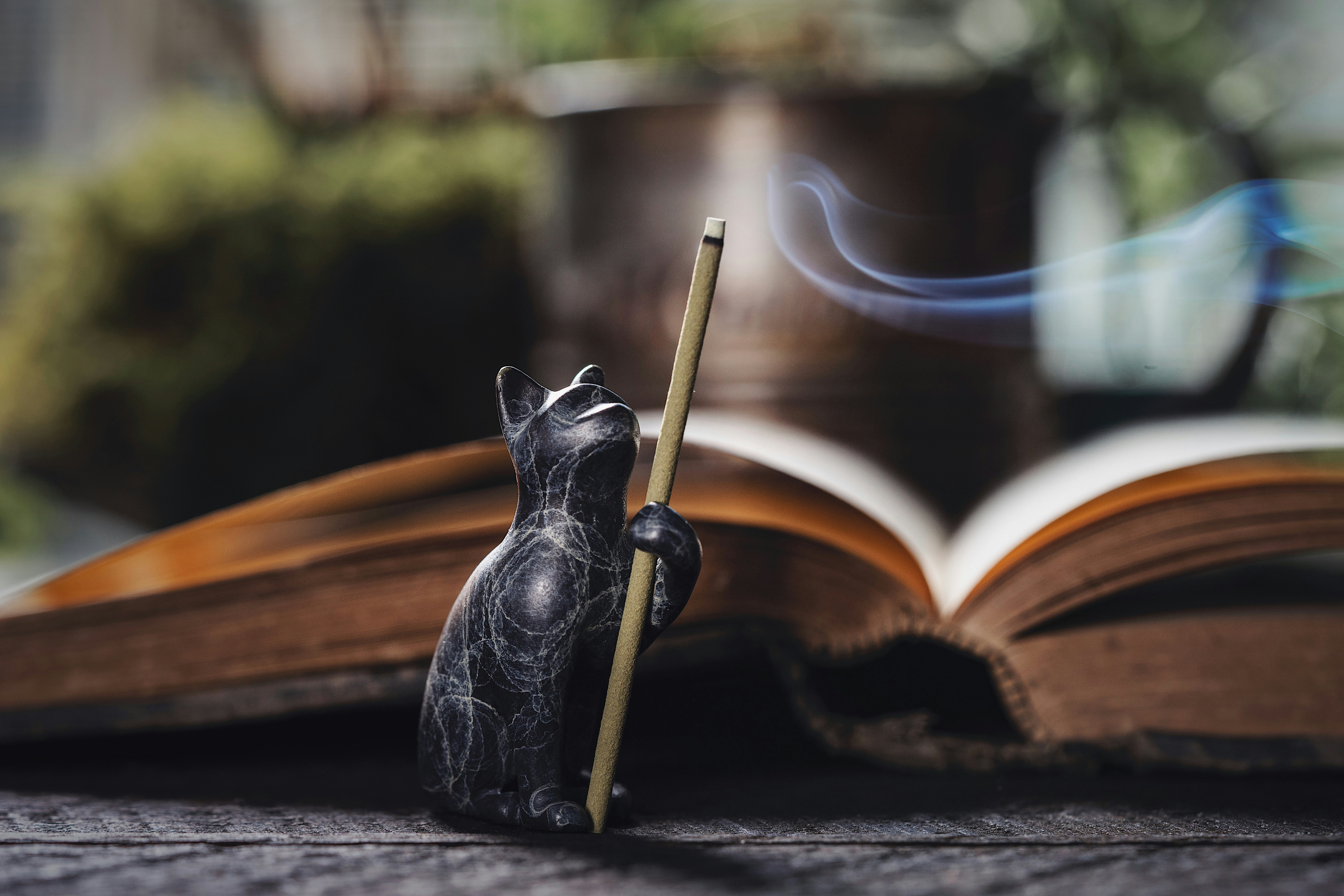 A black cat figurine holding a incense stick next to an open book photo ...