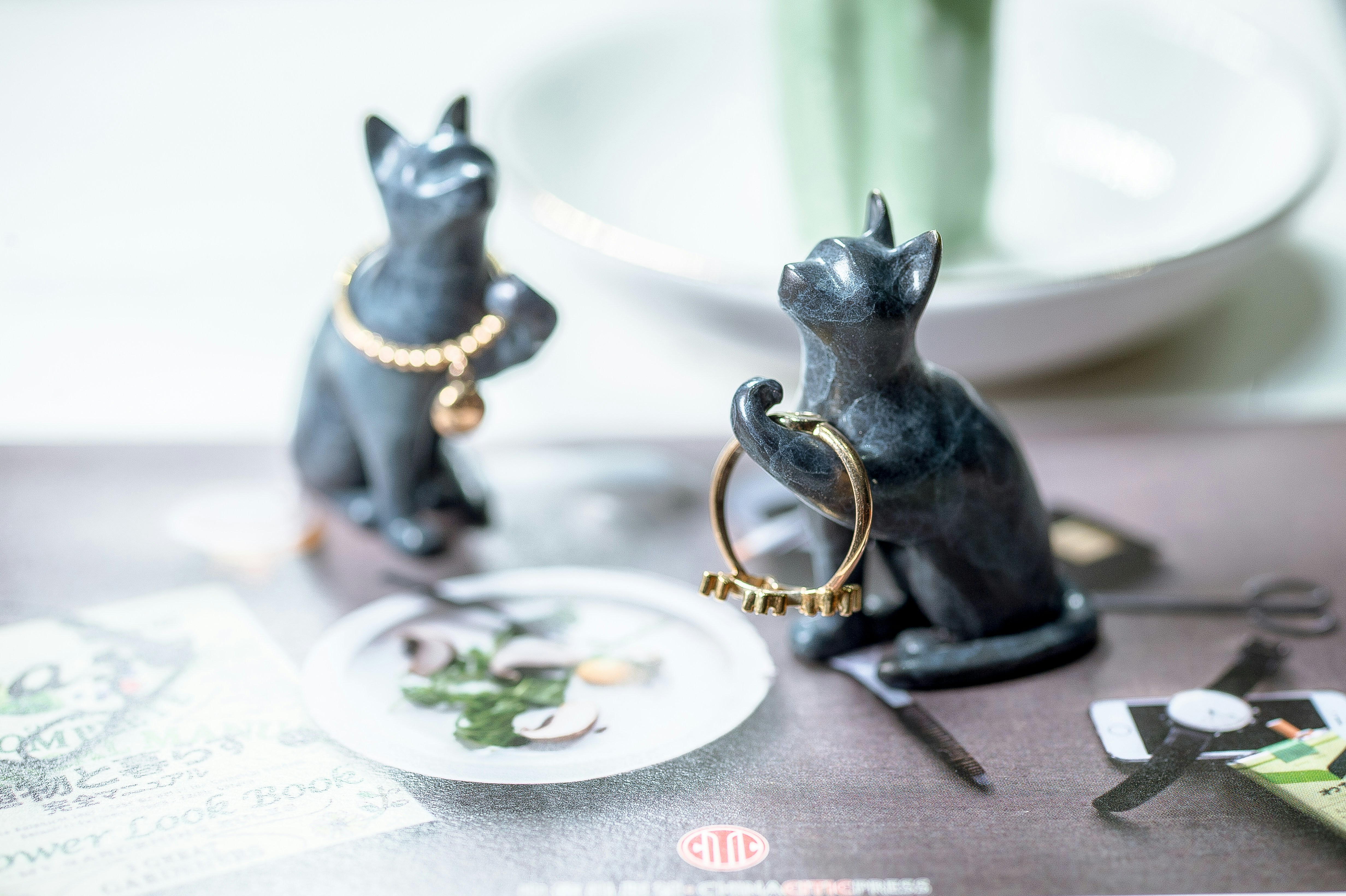 Two cat figurines cradle golden rings amid scattered ephemera