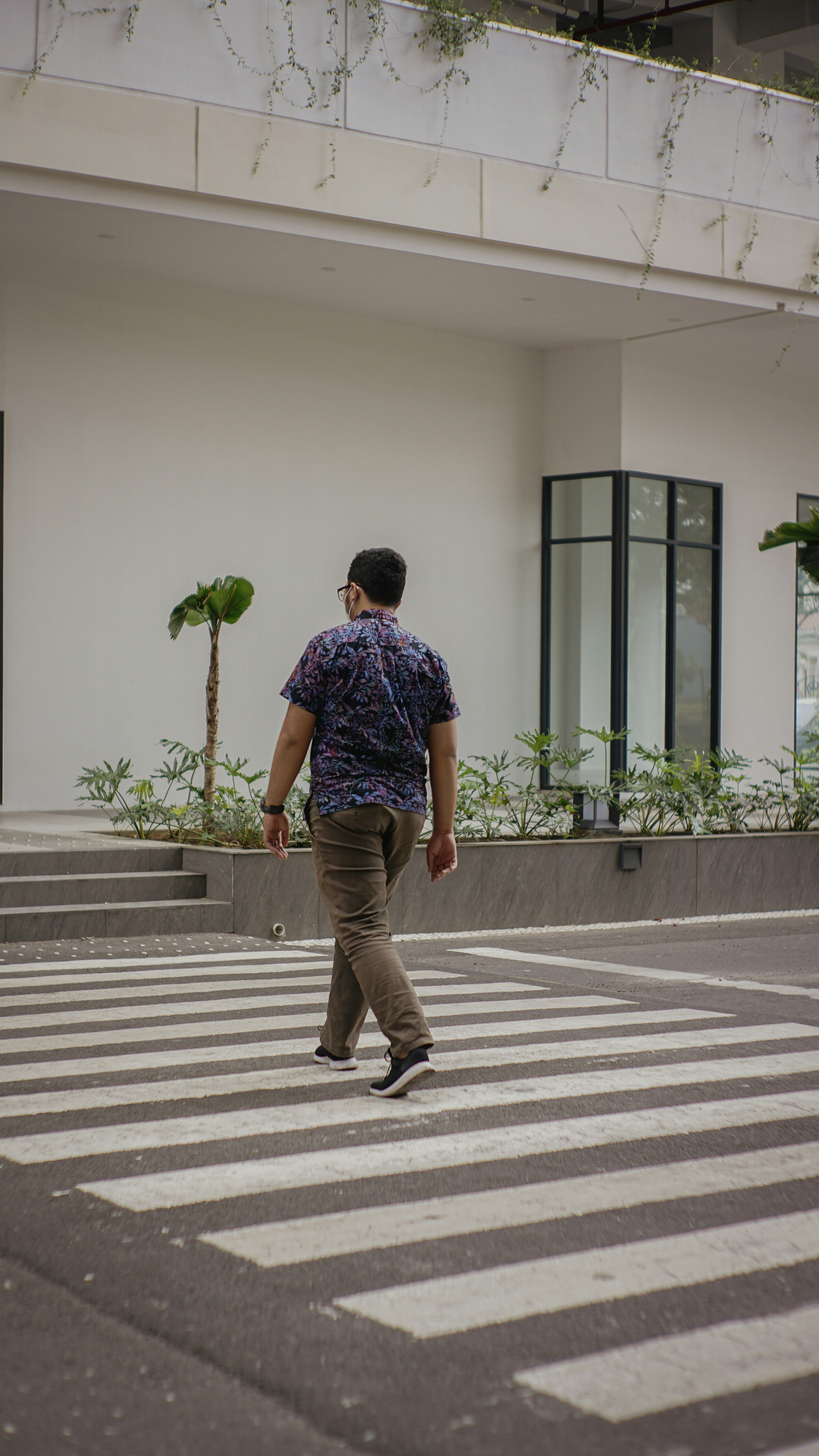 A man walking across a cross walk in front of a building photo – Free ...