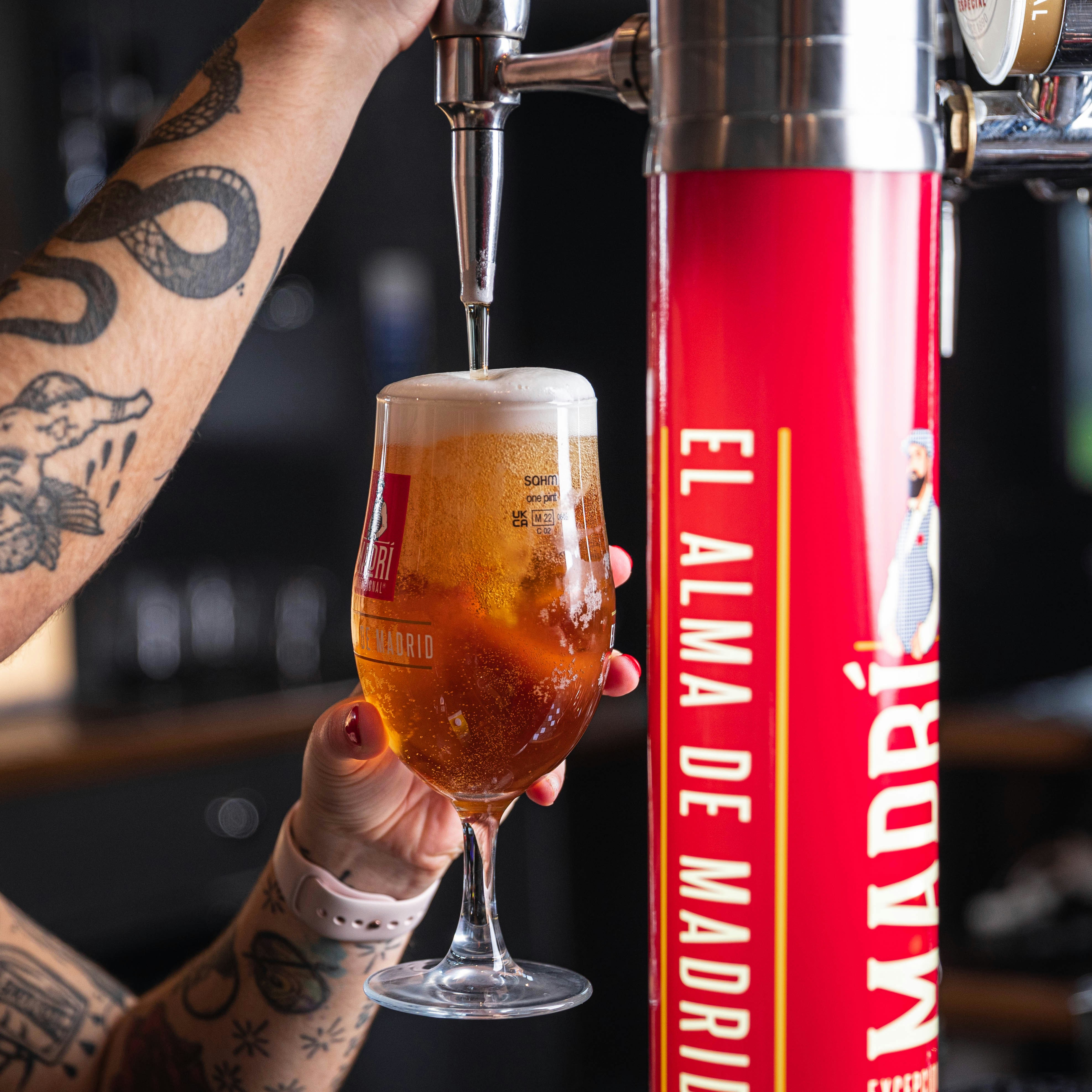 A bartender skillfully pours a frothy beer into a glass, showcasing the rich amber color and bubbly texture against a vibrant tap handle. 