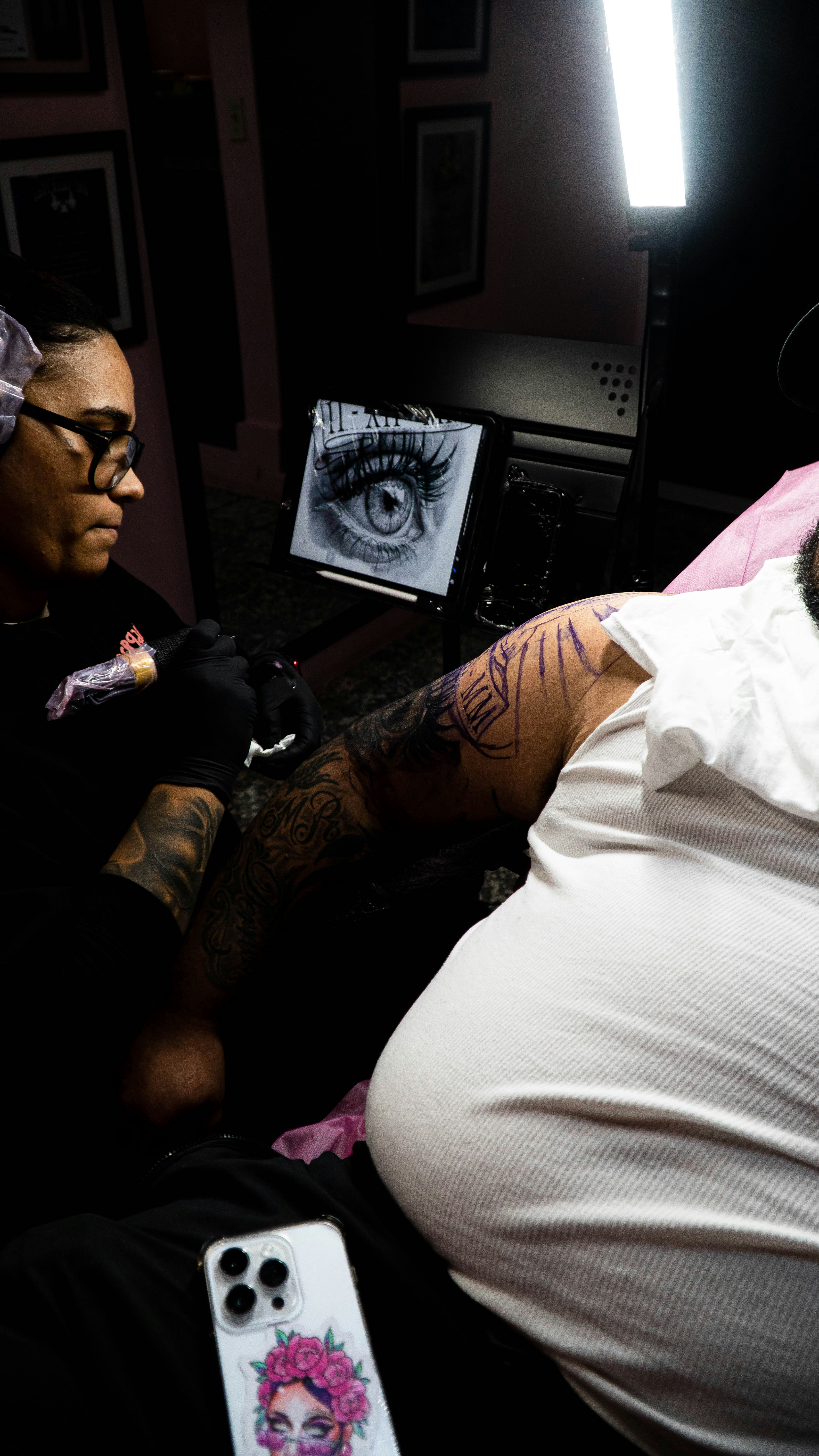 Inking Session: Tattoo Artist at Work beside a Tattooed Arm and Sketch Display