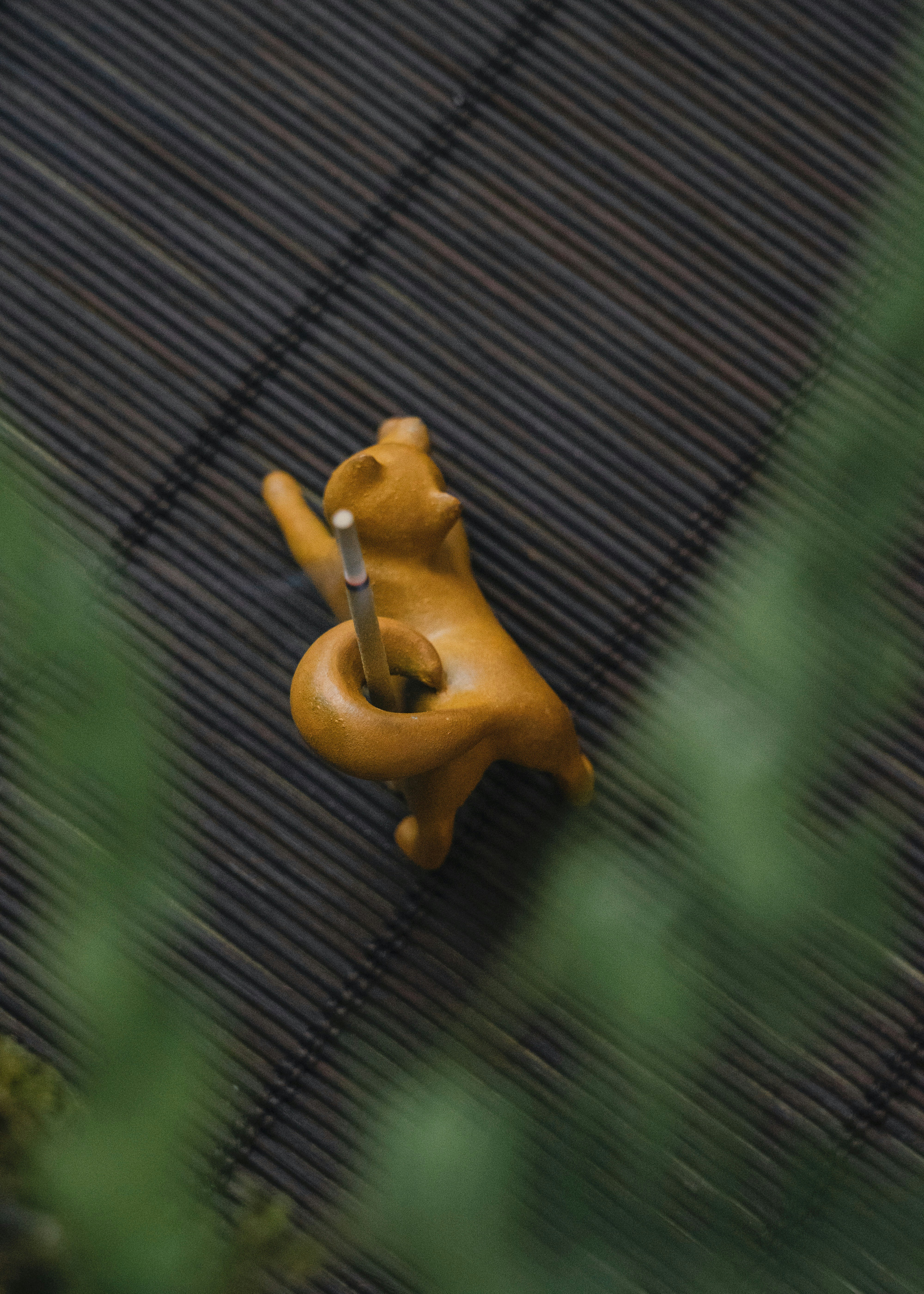 Miniature Ember: An Orange Clay Figure Gripping a Cigarette on a Striated Deck