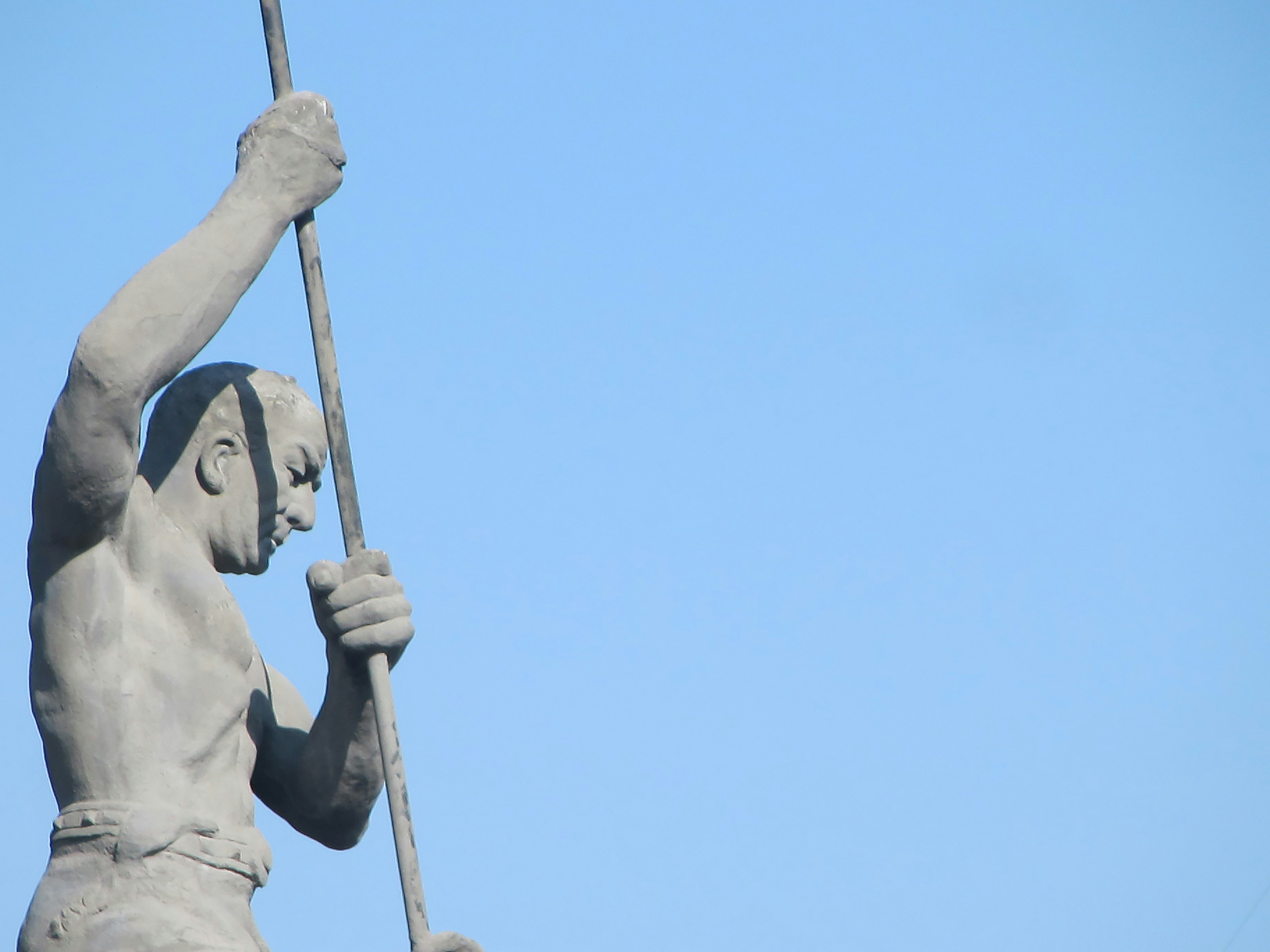 A towering sculpture of a laborer gripping a pole against a clear blue sky, symbolizing strength and resilience.