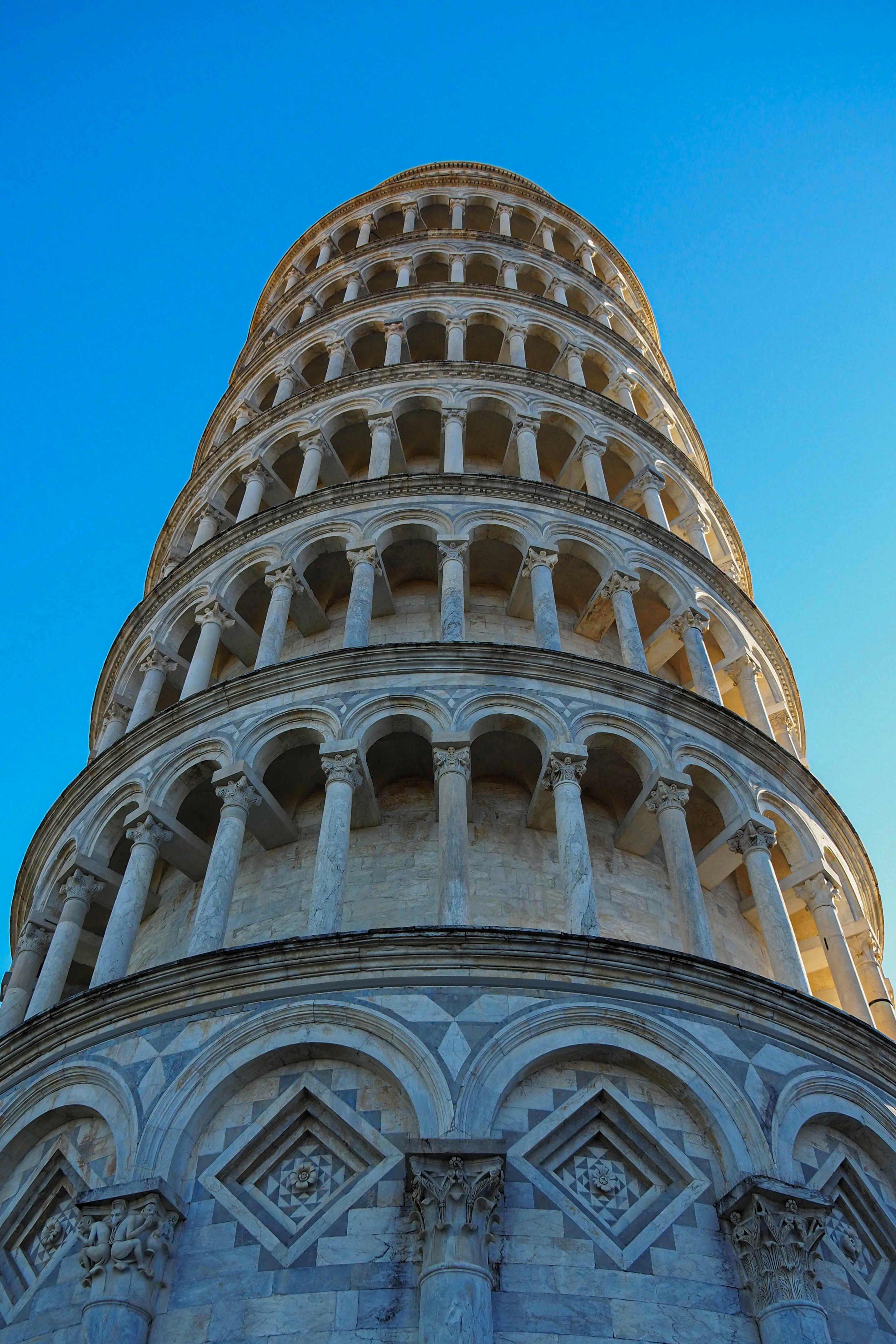 The Leaning Tower of Pisa rises majestically against a clear blue sky, showcasing its intricate arches and columns.