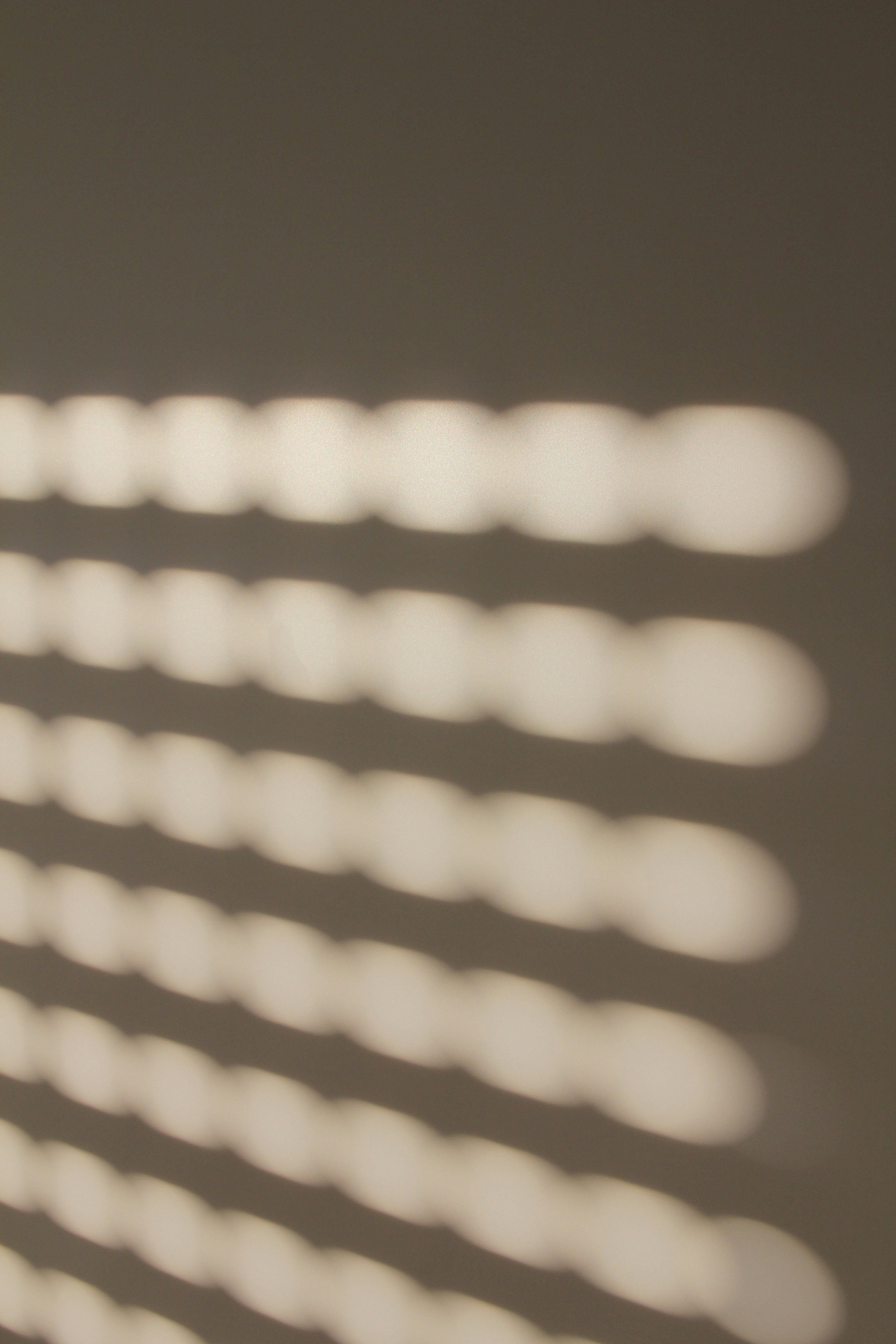 Soft, diffused light creates parallel stripes across a neutral wall.