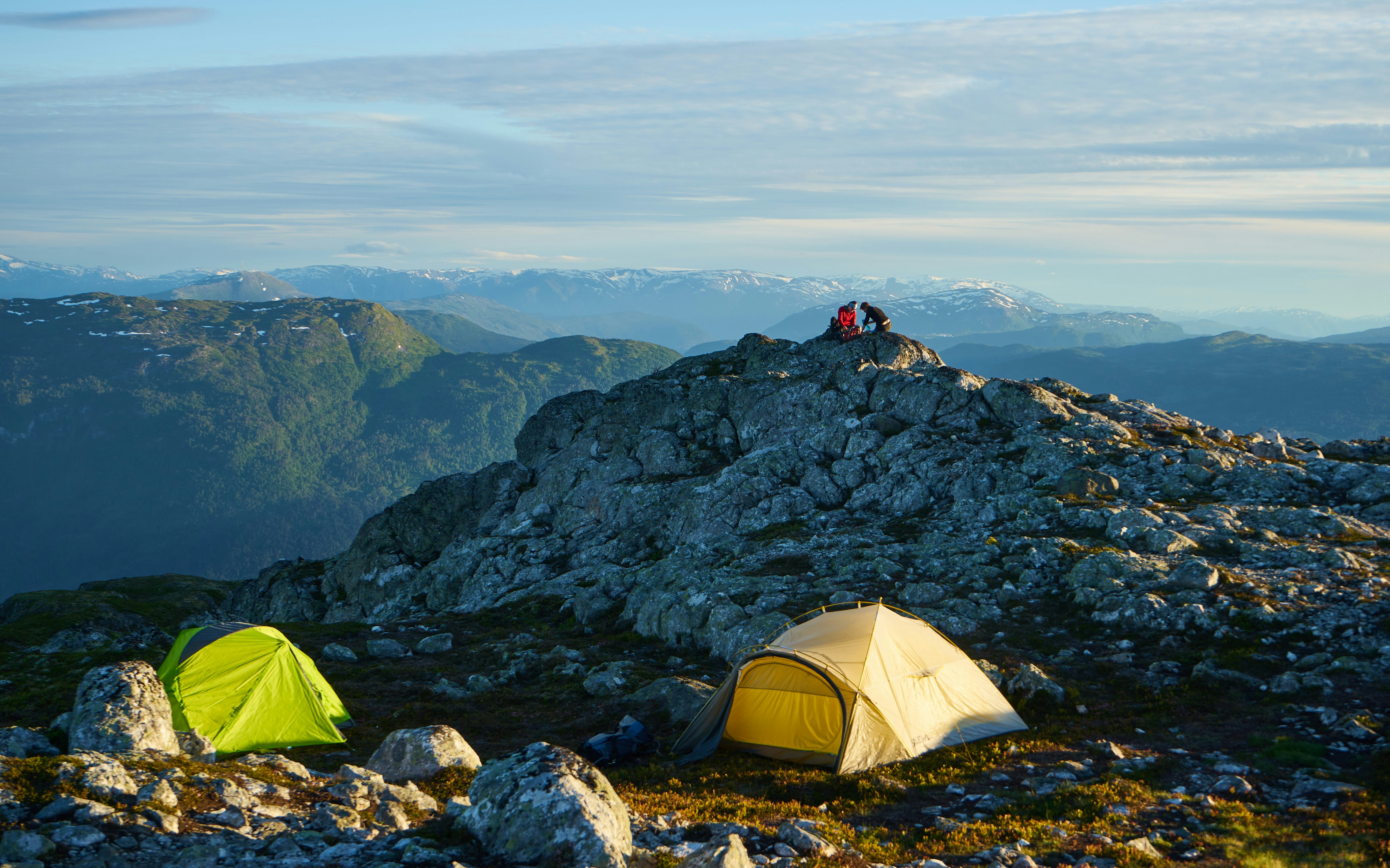 This is camping in Norway: two people preparing their dinner after setting up the tents. | a couple of tents sitting on top of a mountain