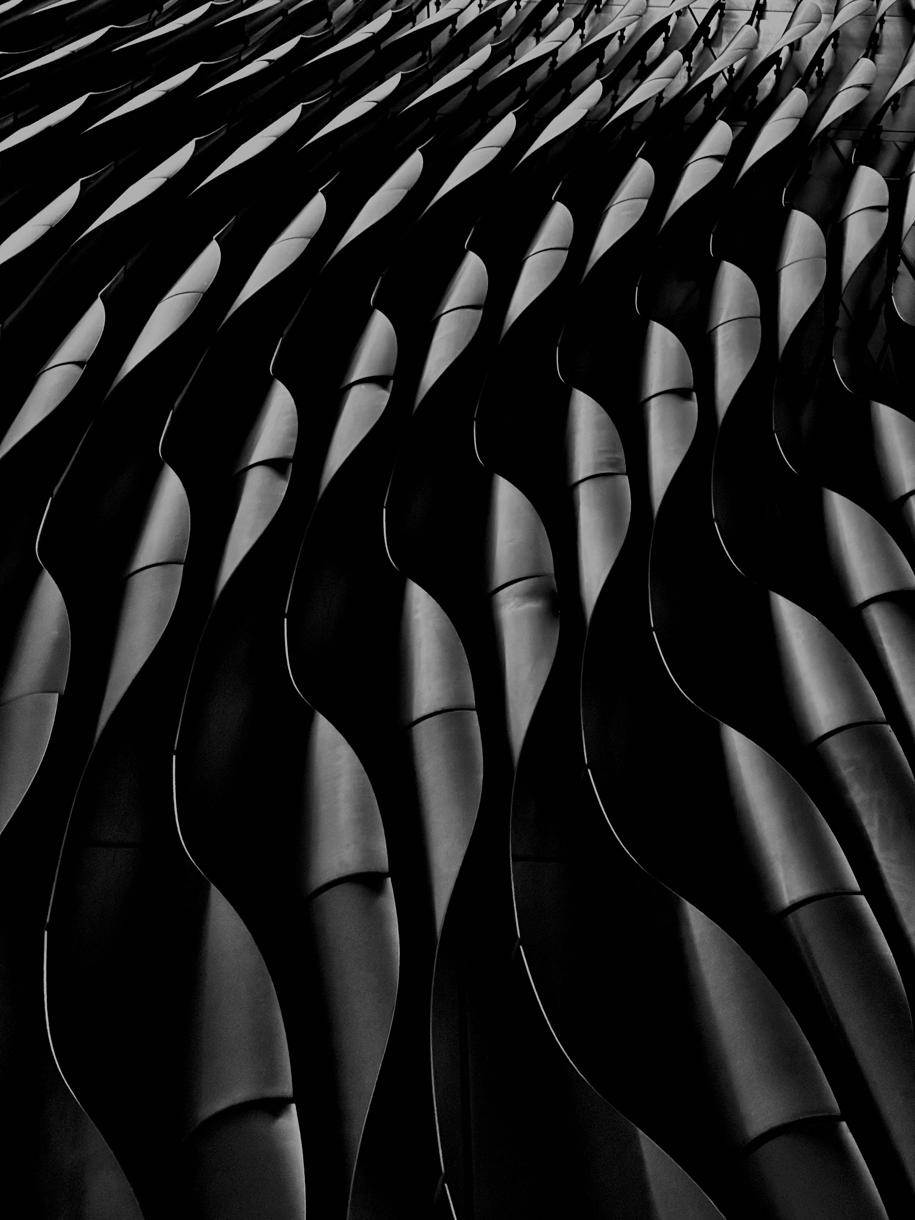 Close-up of repeating curved steel panels forming a wave-like abstract texture in high-contrast black and white.