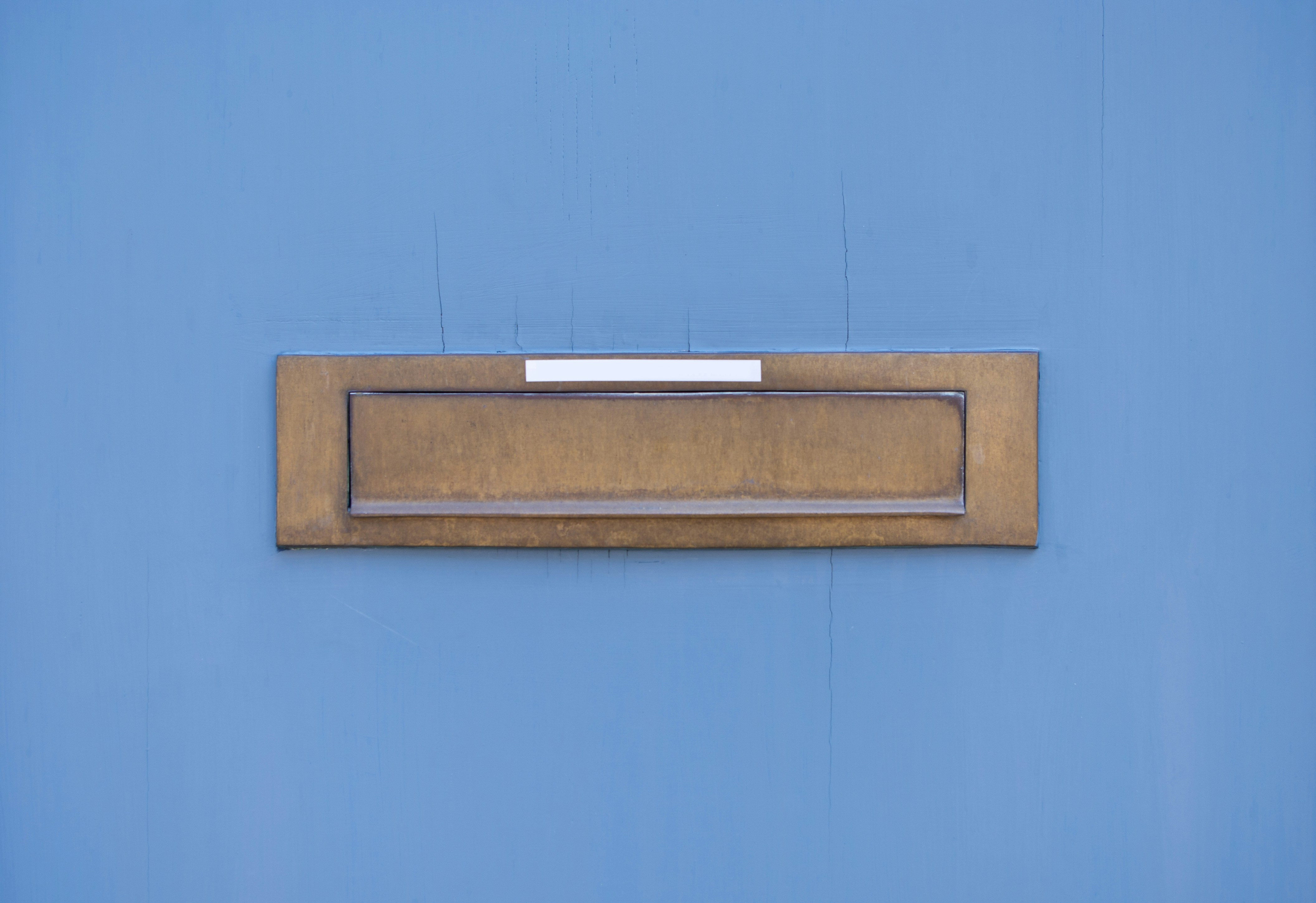 Rectangular metal vent centered on a smooth blue wall, with a small white strip above and weathered edges.