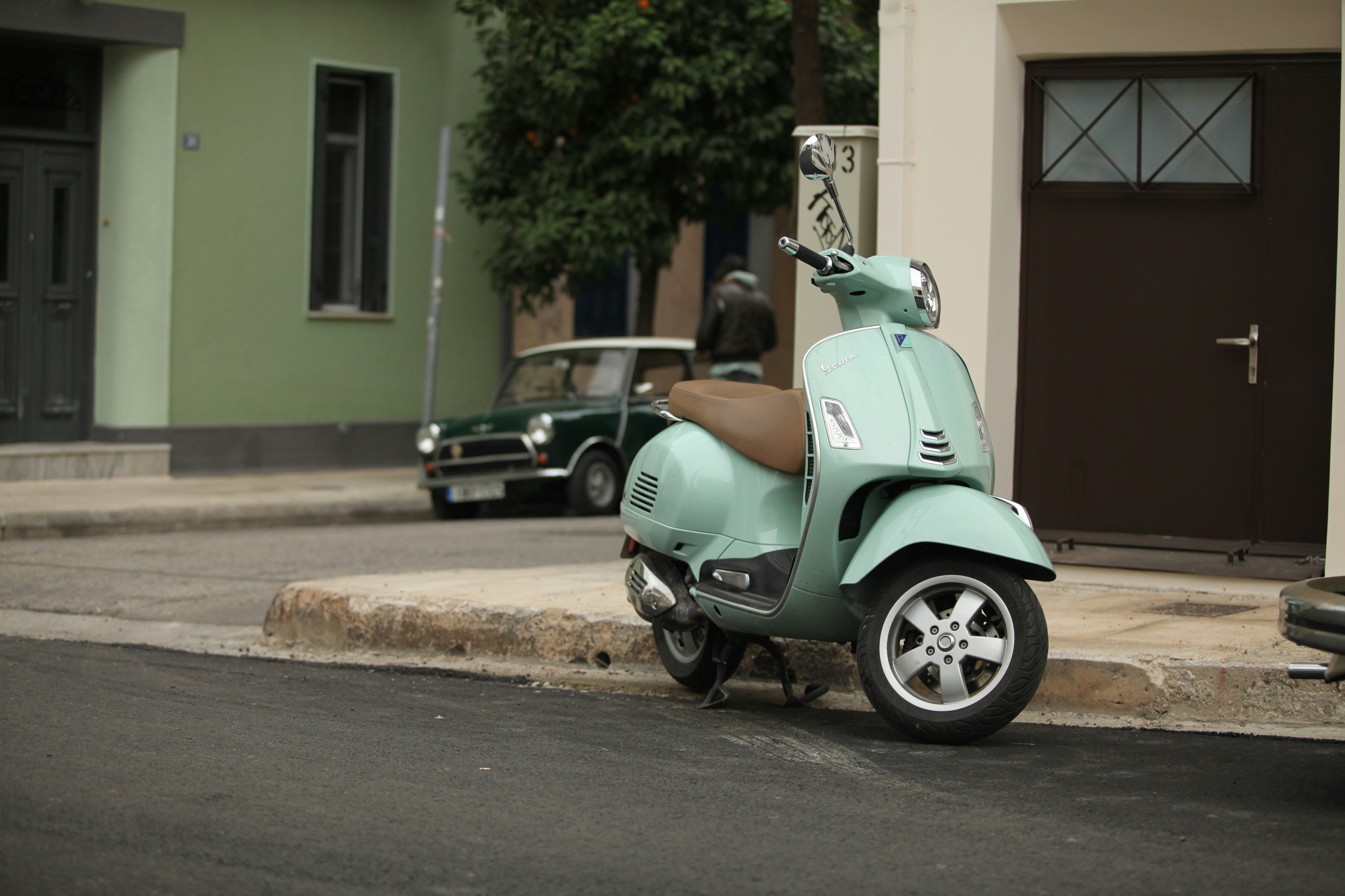 Mint green scooter parked on a city street corner beside a vintage car.