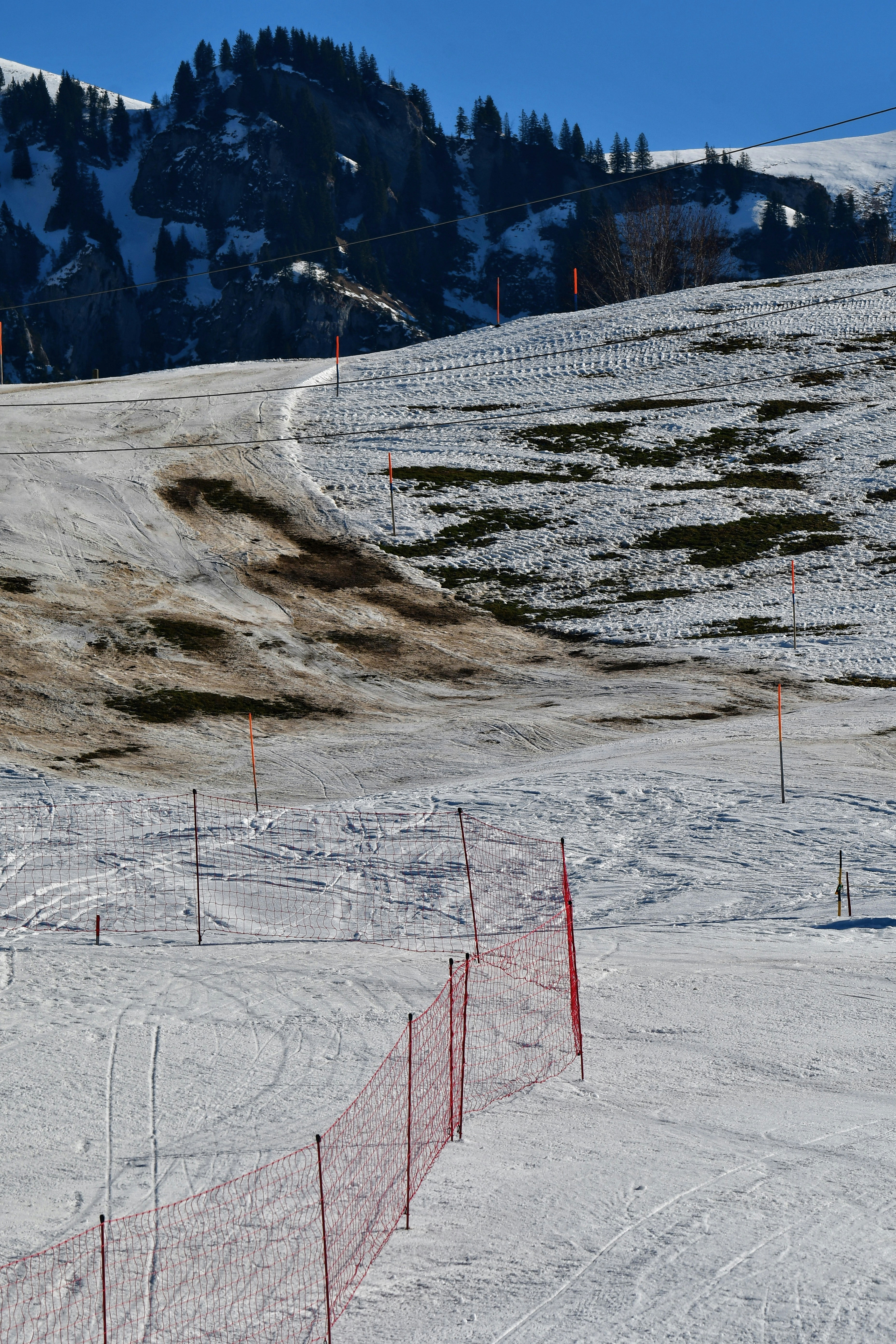 Snow-dusted slope with safety fencing under a clear alpine sky