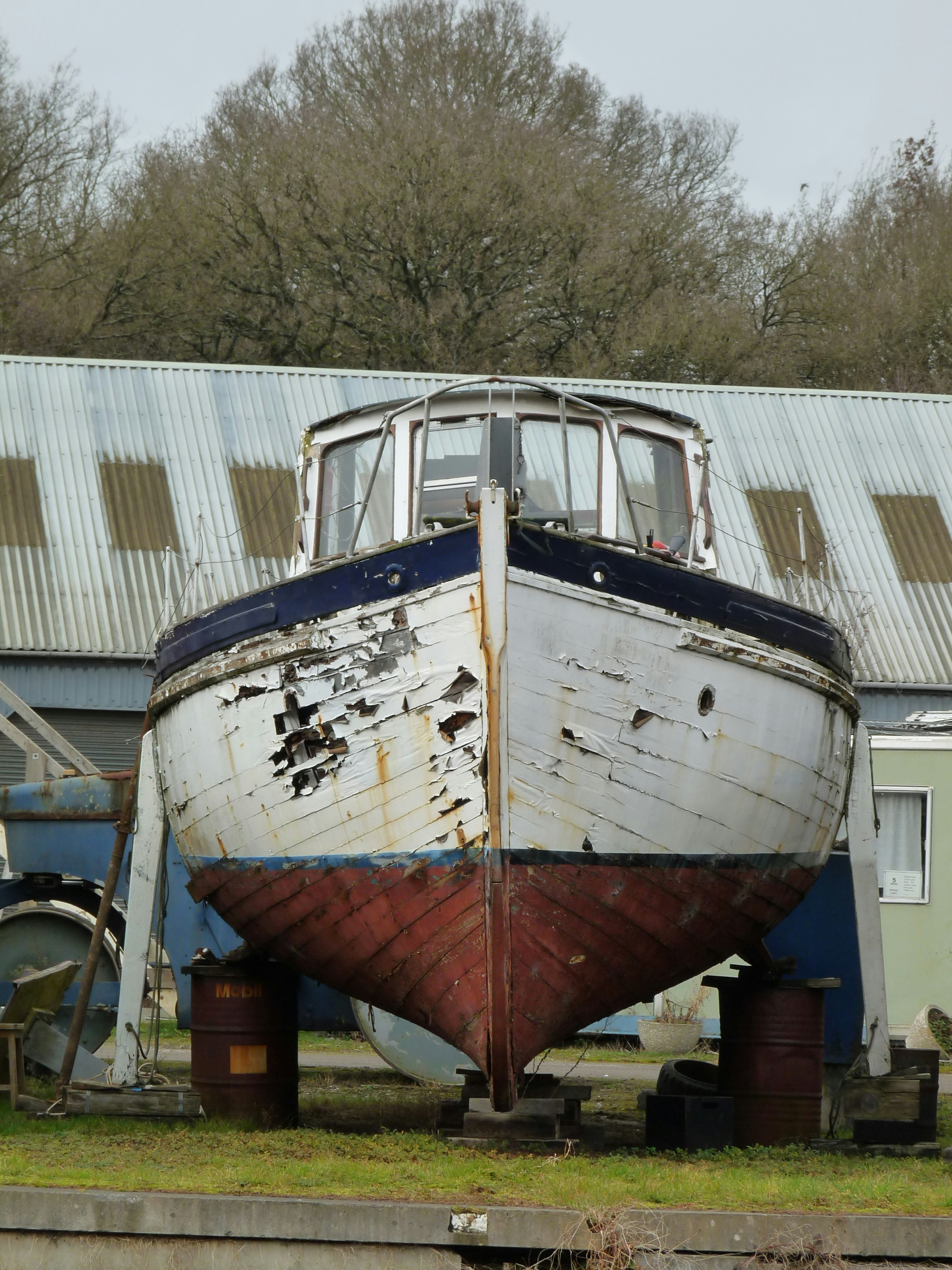 Weathered boat resting on land, showcasing peeling paint and rust against a backdrop of industrial buildings. 