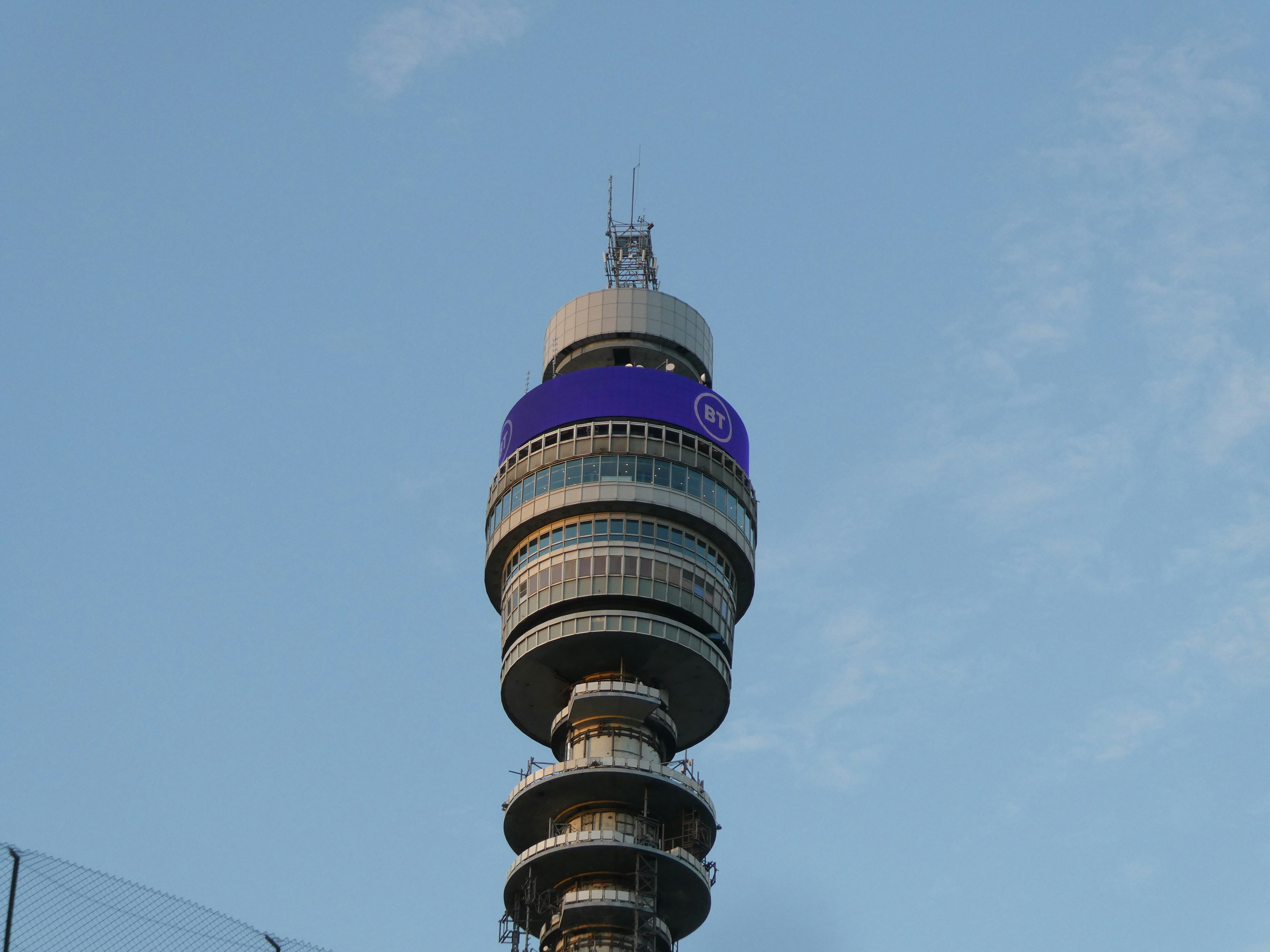 A telecommunications tower soaring against a clear sky, showcasing its unique cylindrical design and vibrant signage.