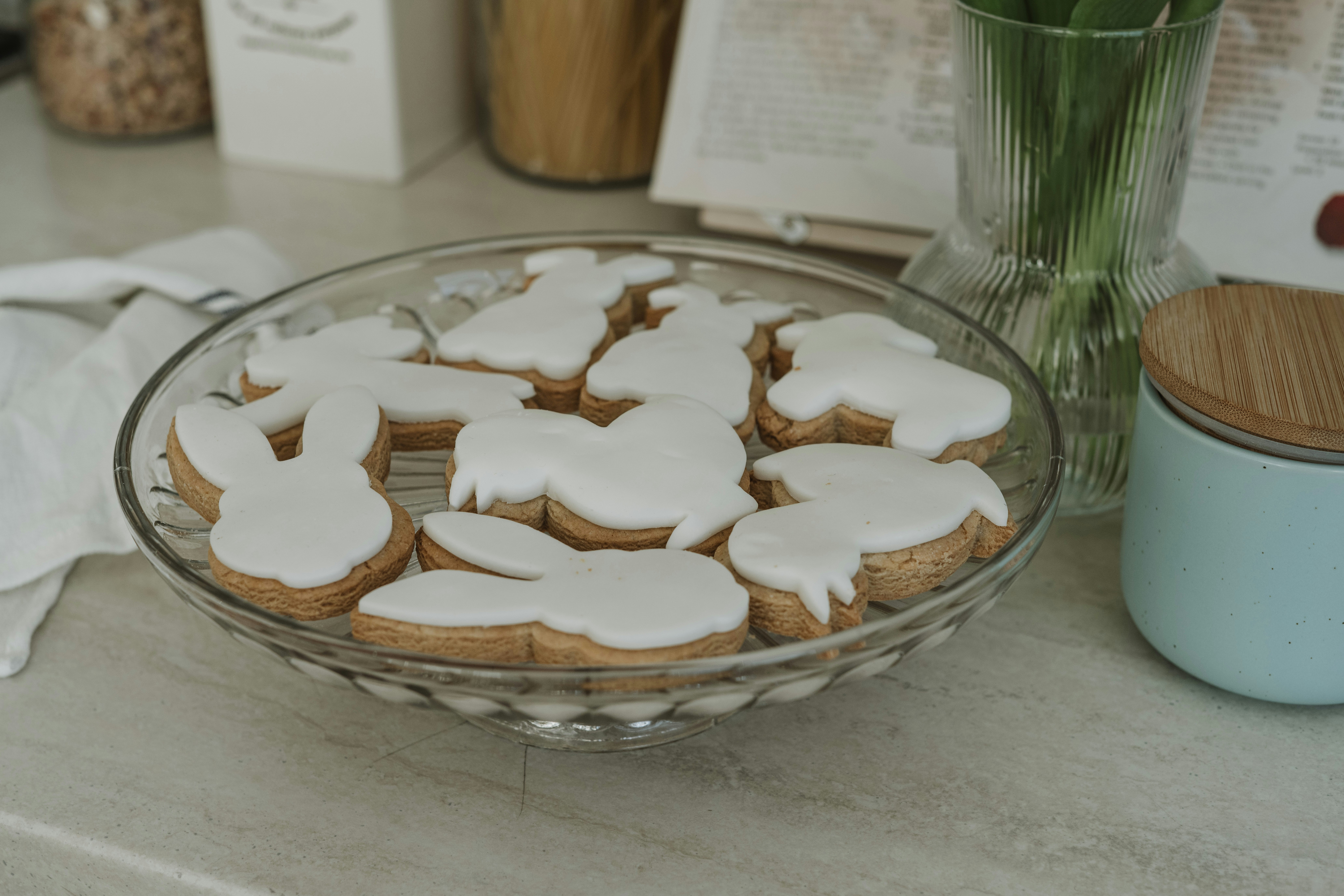 Bunny-shaped iced cookies in a glass dish amid a cozy kitchen counter scene