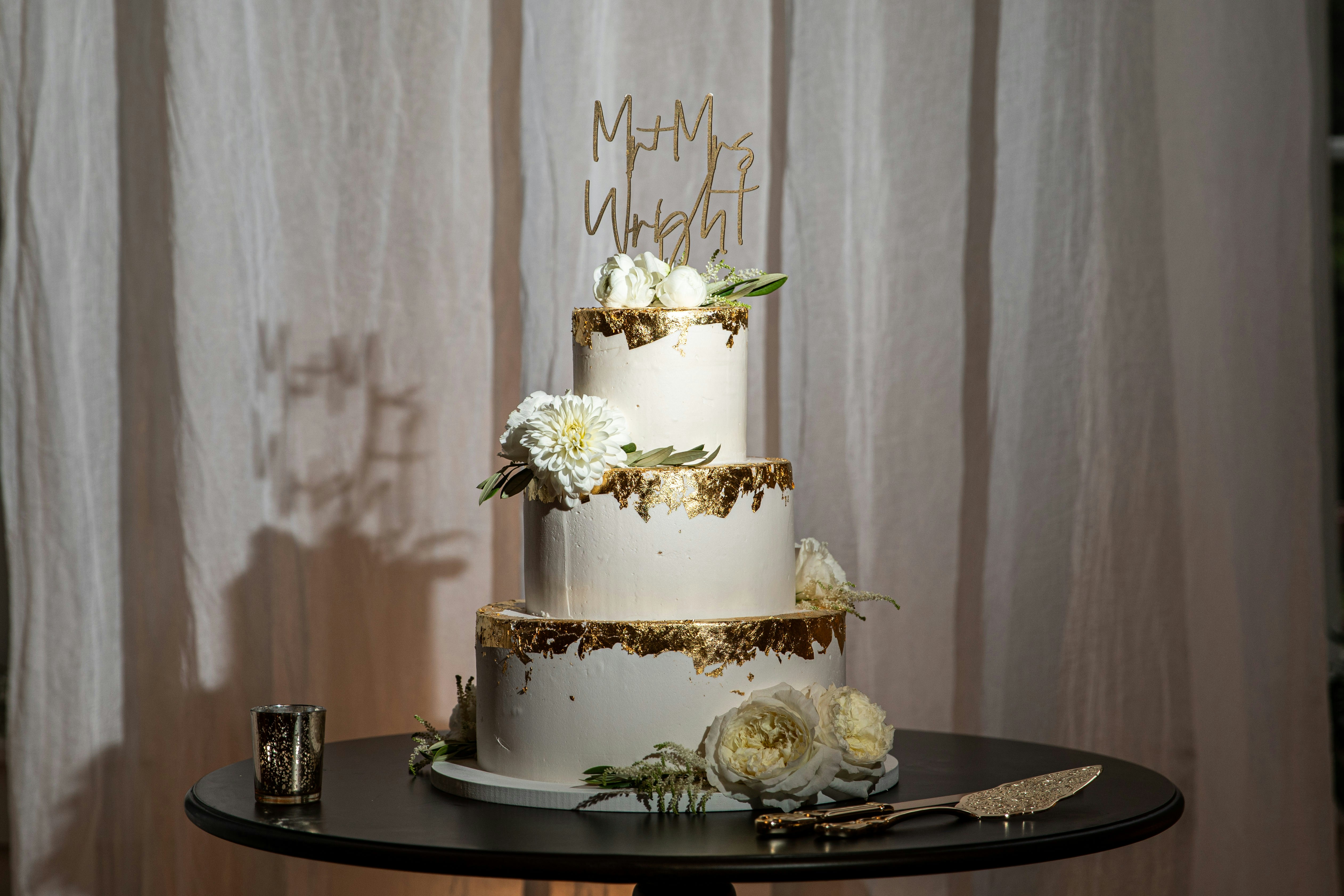 A three tiered cake with white flowers on a table photo – Free ...