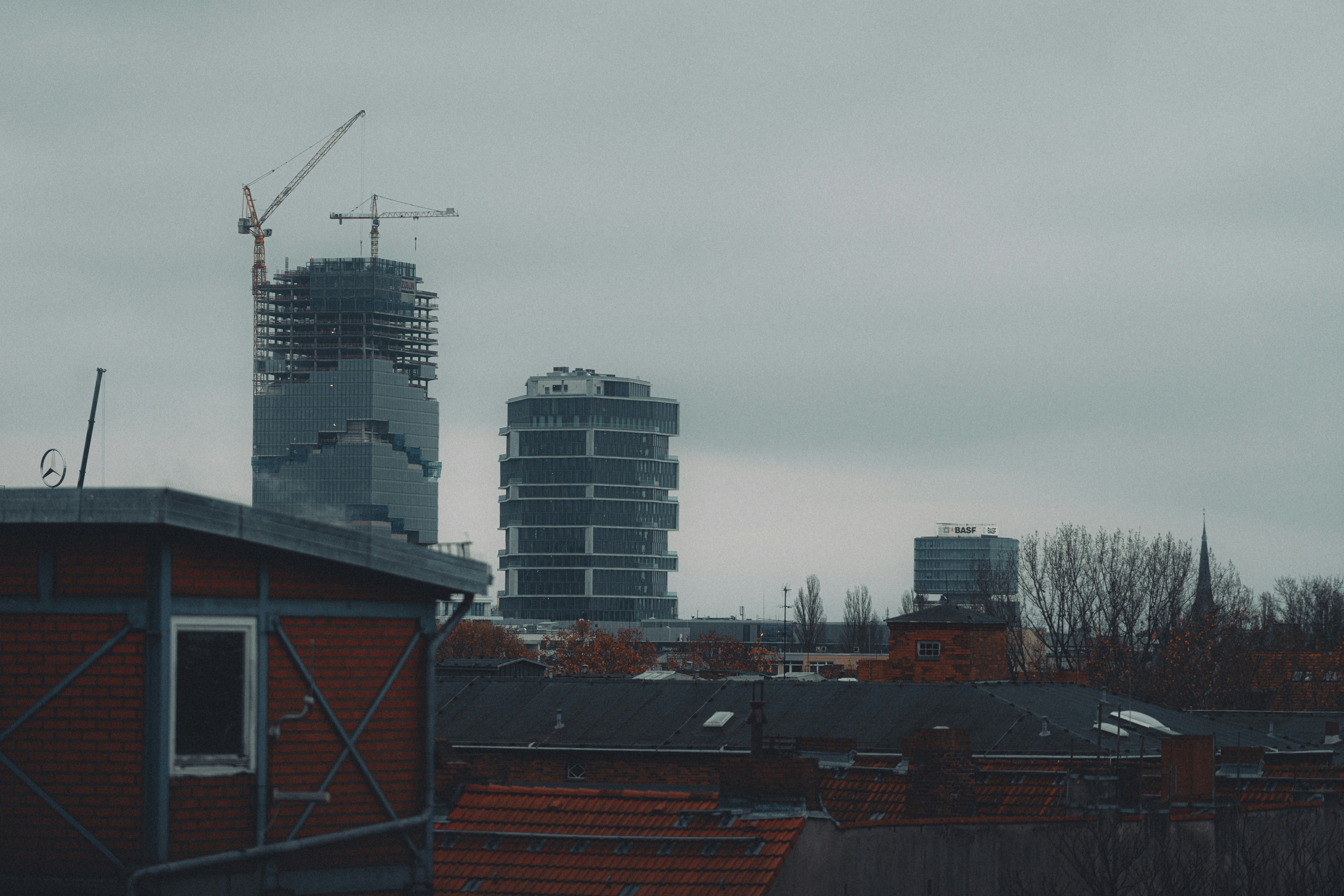 Skyscrapers with cranes rise above rooftops against an overcast sky.