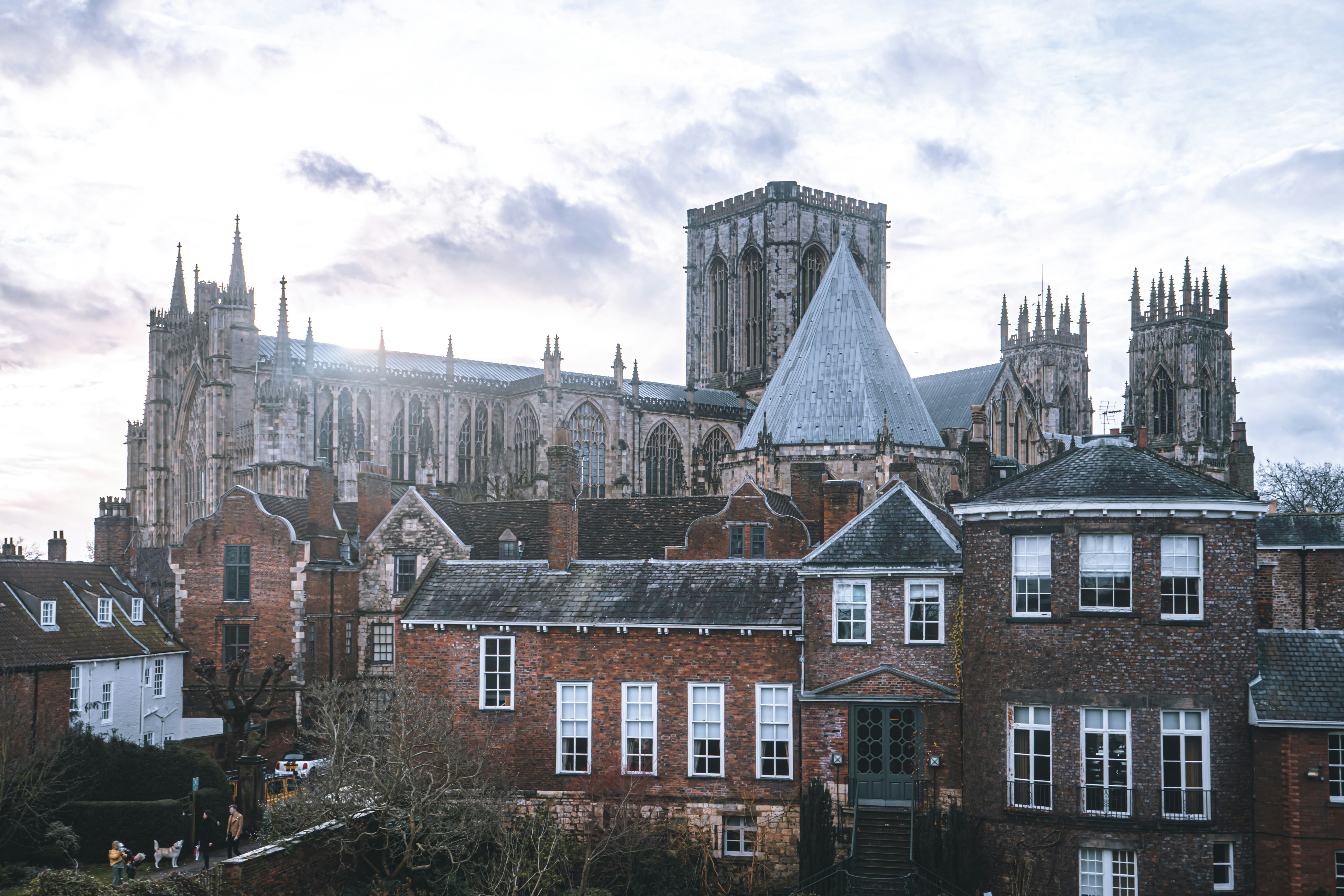 Historic cathedral towers over a cluster of red-brick buildings under a cloudy sky.