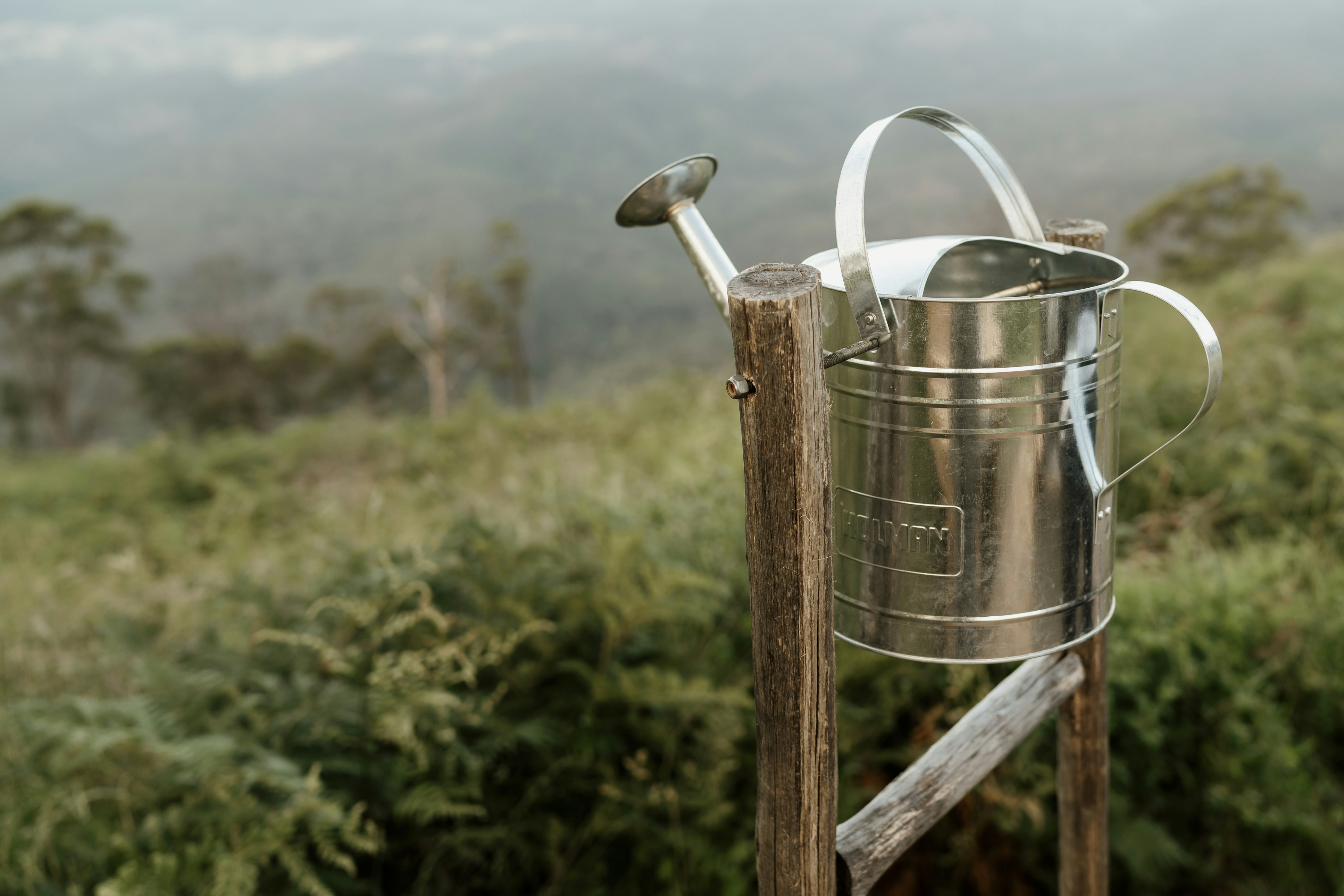 Galvanized watering can on a weathered post overlooking a misty hillside