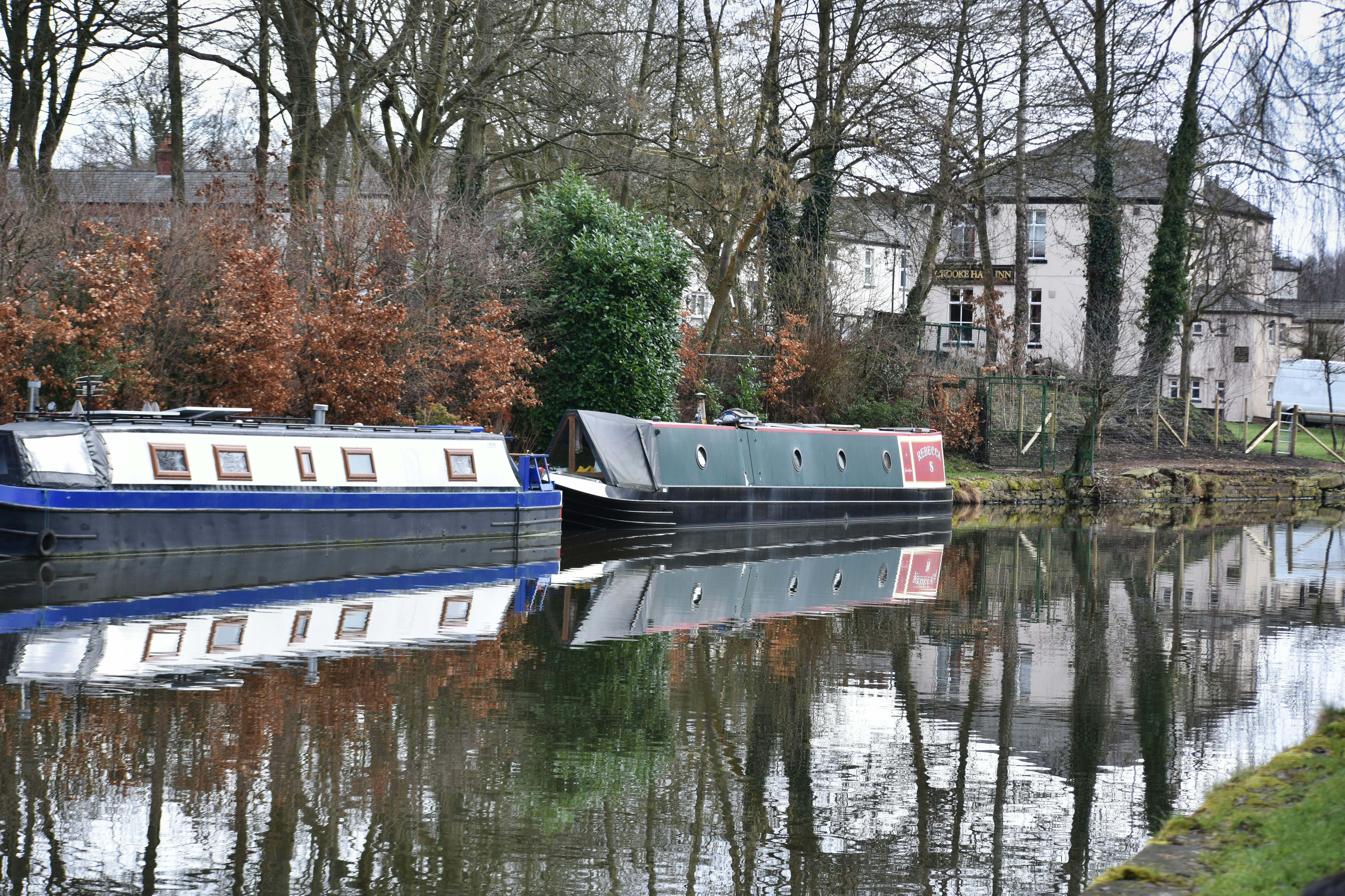 Canal boats moored beside a calm, reflective waterway with bare winter trees and a distant house.