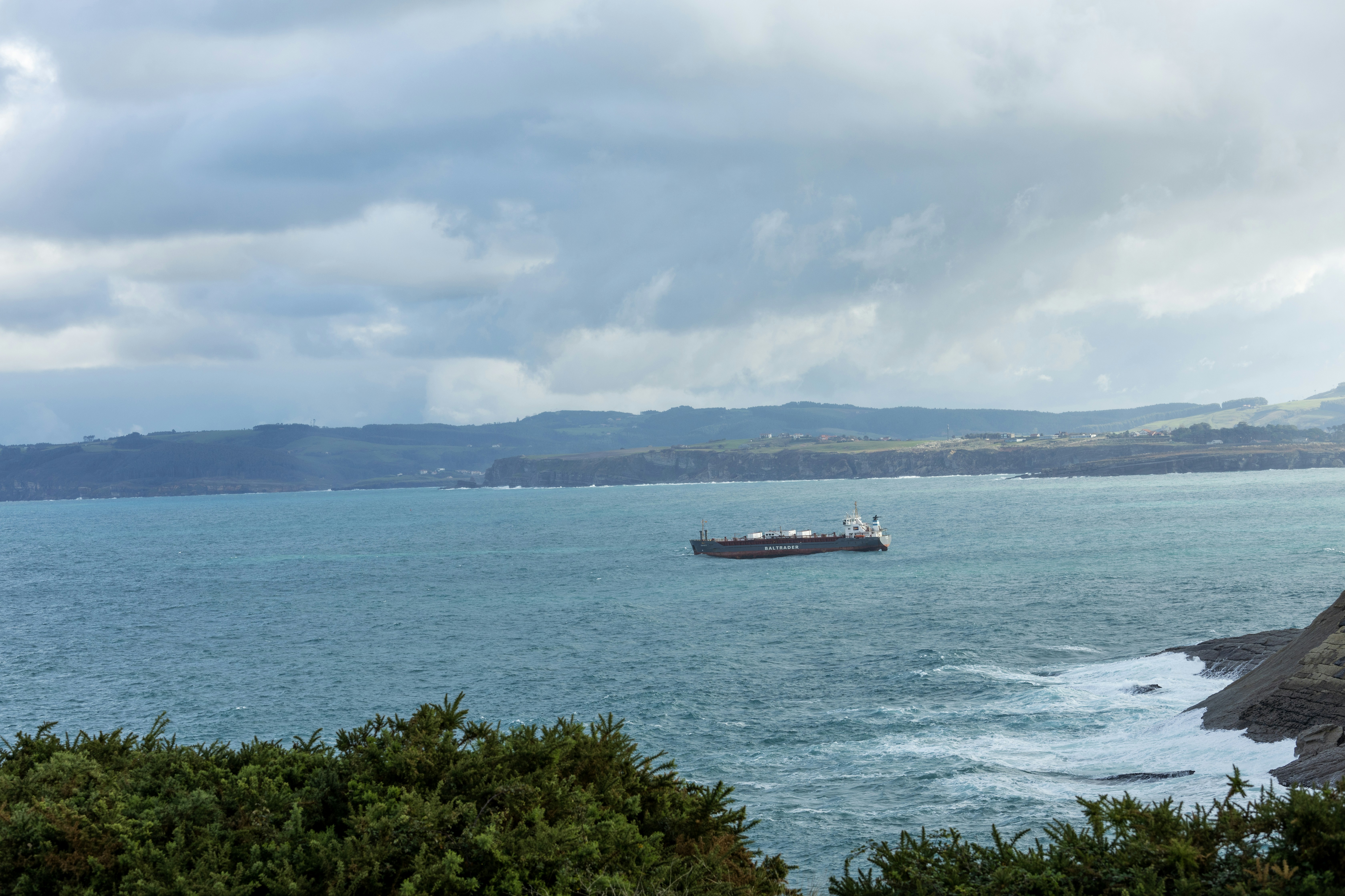 A lone cargo barge drifts along a quiet coastal ribbon