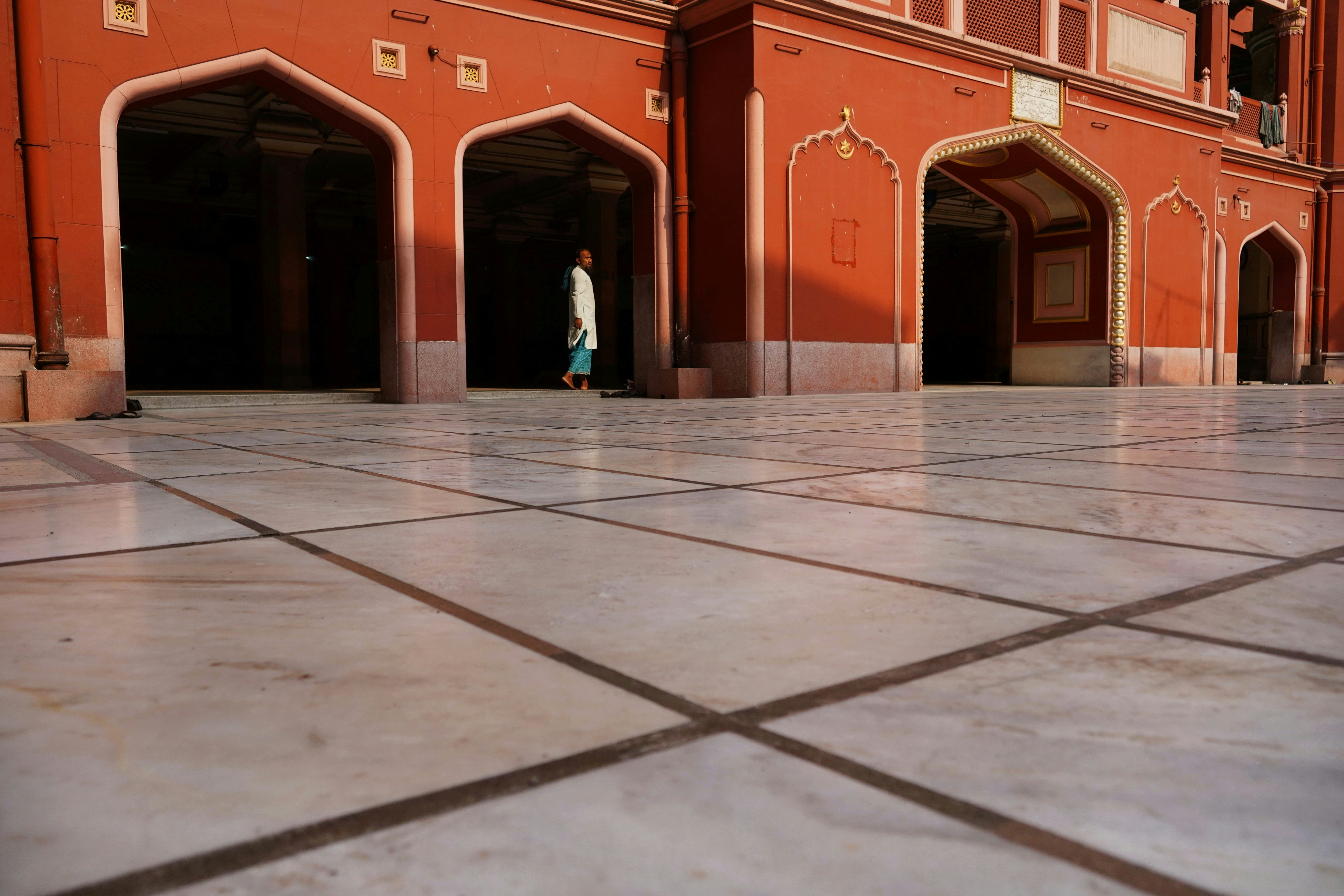 Echoes in the Courtyard: A Single Figure Beneath Crimson Arches