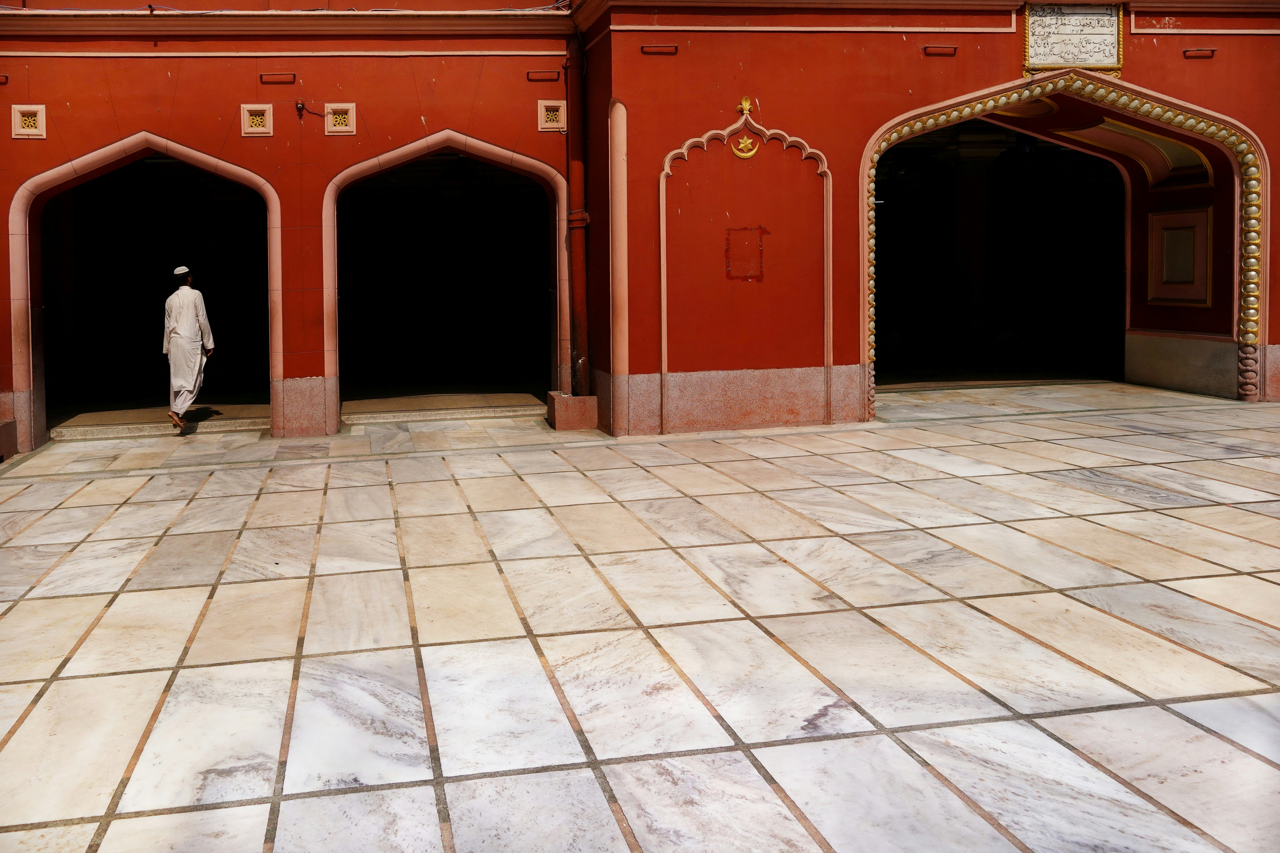 Lone Walker under Red Arches: A Quiet Moment in a Marble Courtyard