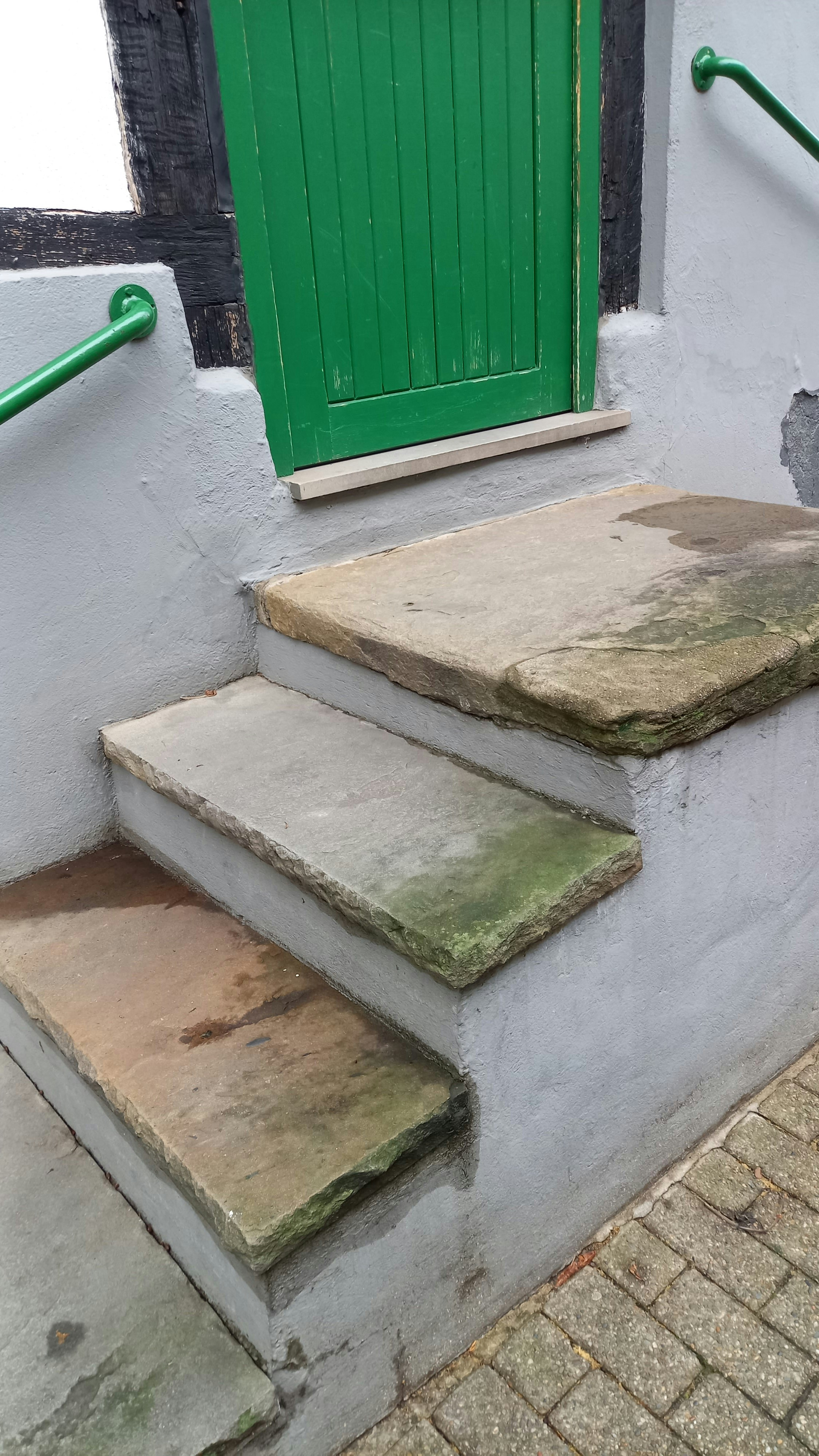 Weathered stone steps leading up to a vibrant green door, showcasing the passage of time and nature's touch. Moss and water stains add character to the scene.