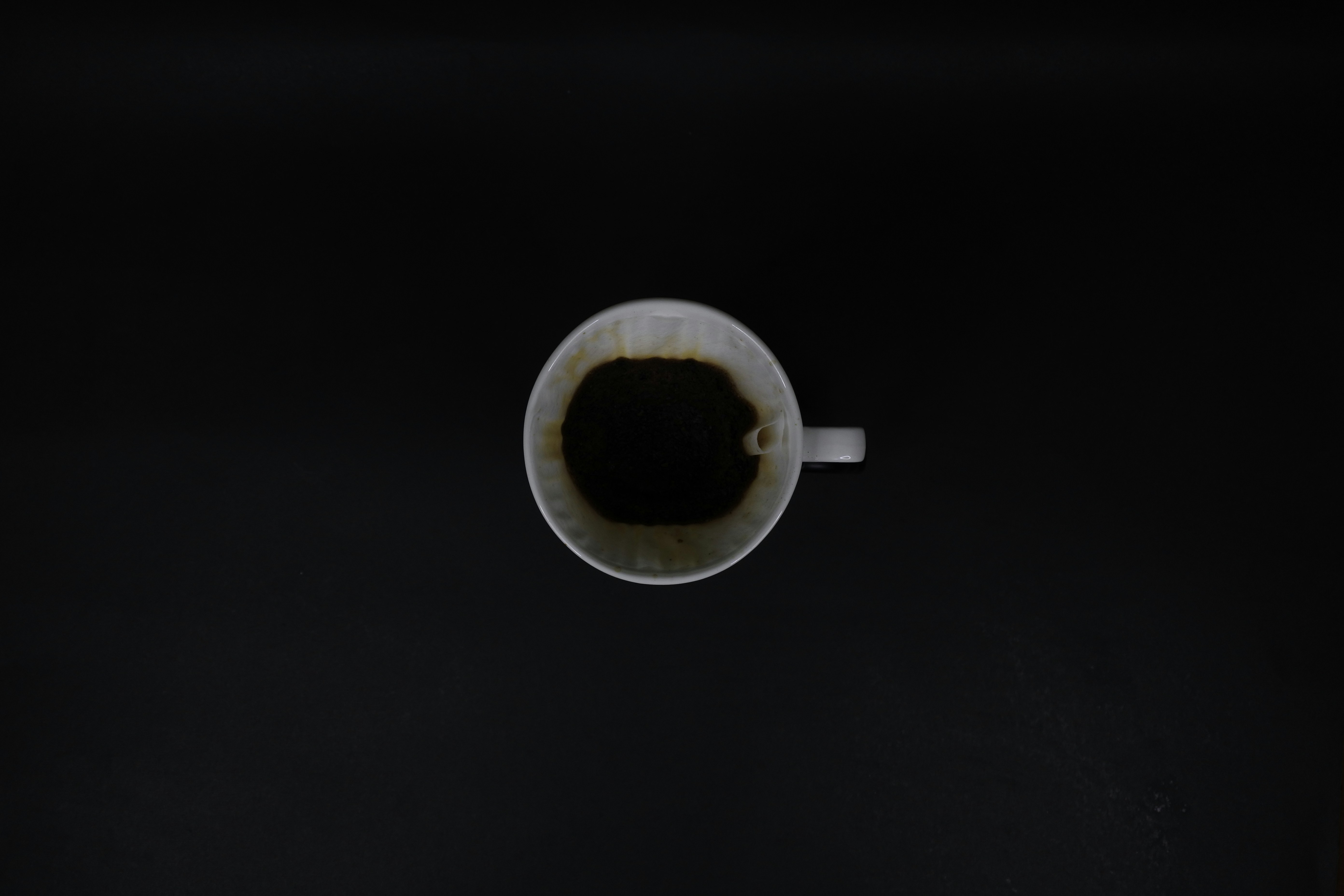 Top-down photograph of a white coffee cup with dark coffee on a matte black surface.