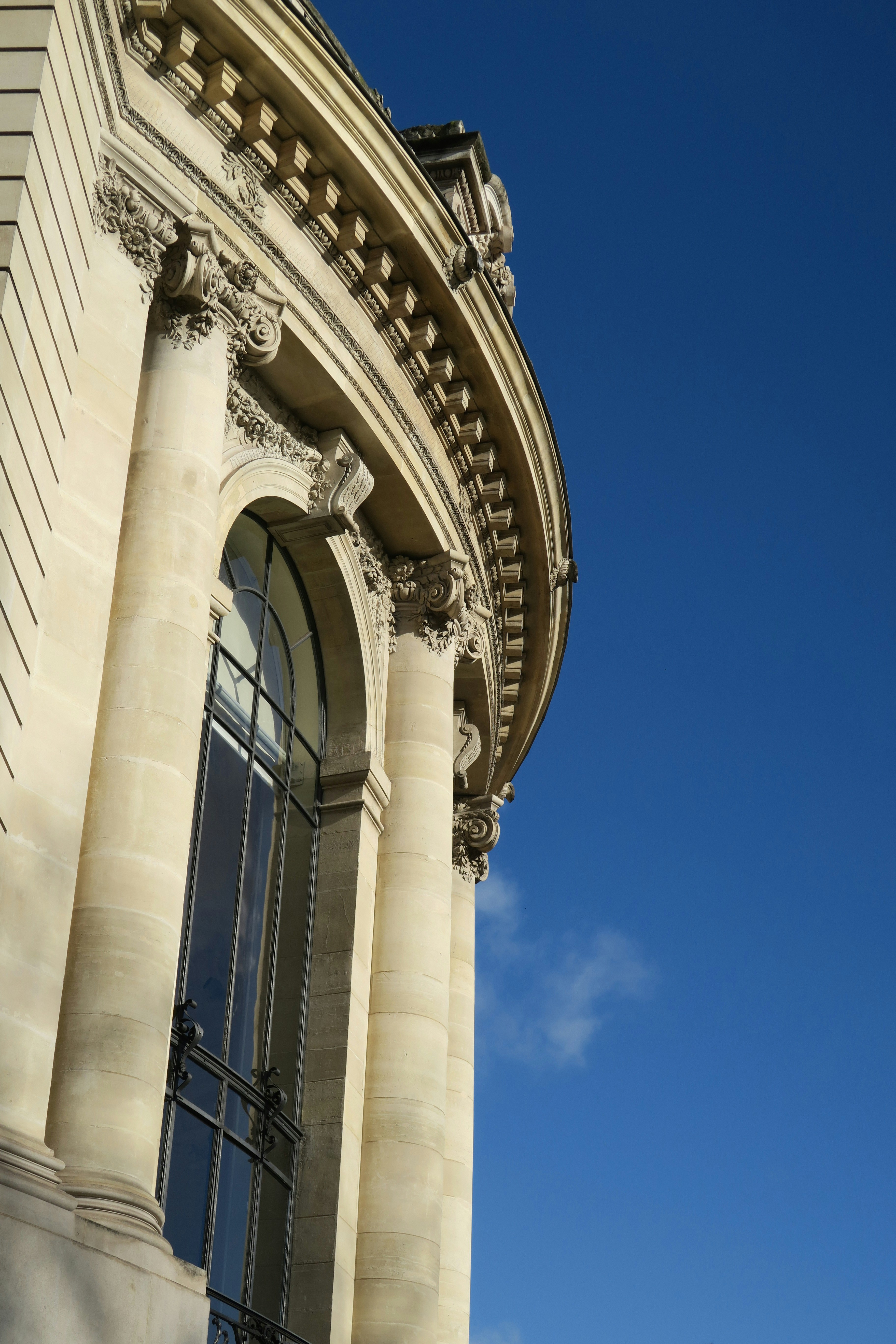 Ornate stone facade of a building with large arched windows set against a clear blue sky.