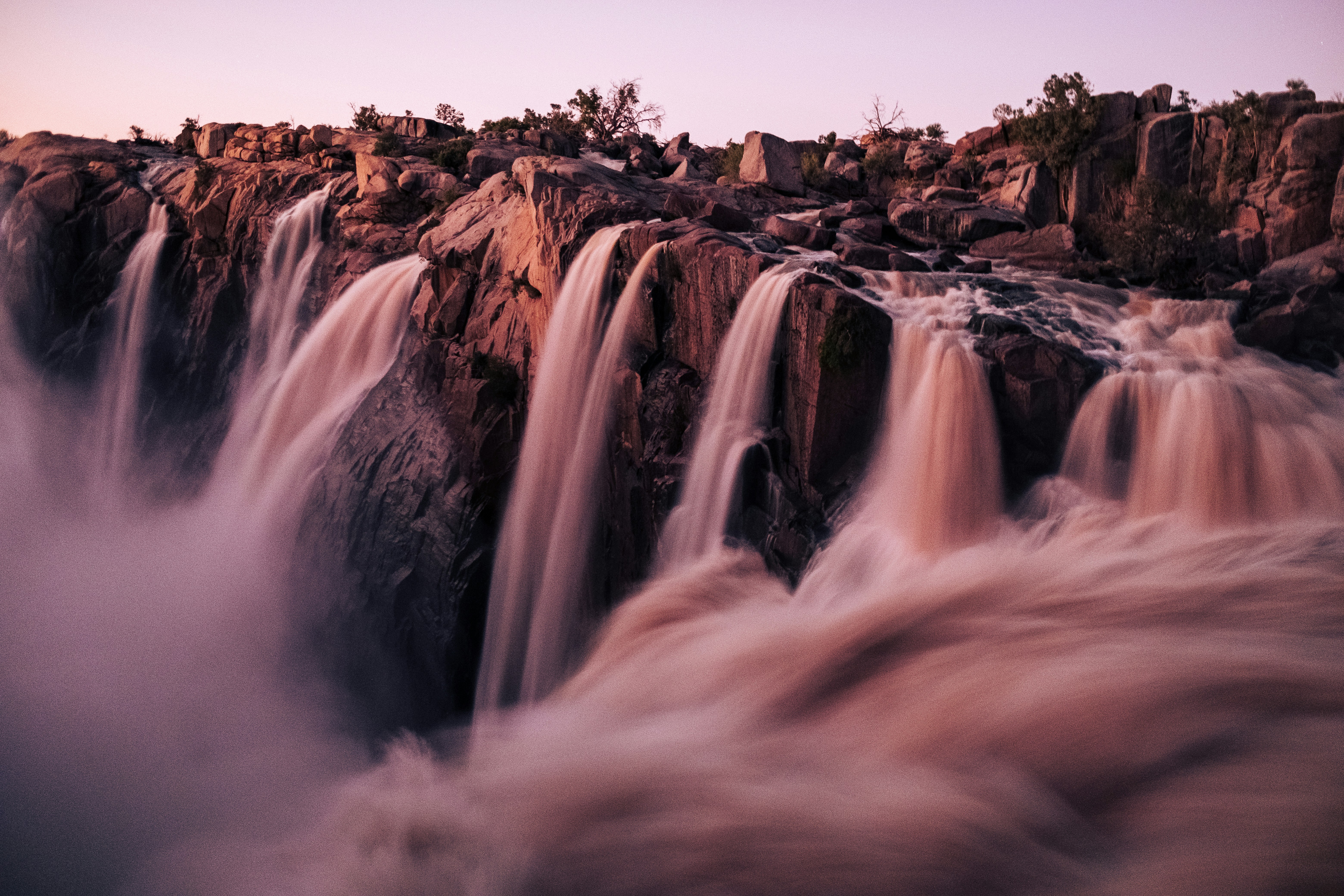 Silky waterfalls cascade over rugged cliffs under a twilight sky.