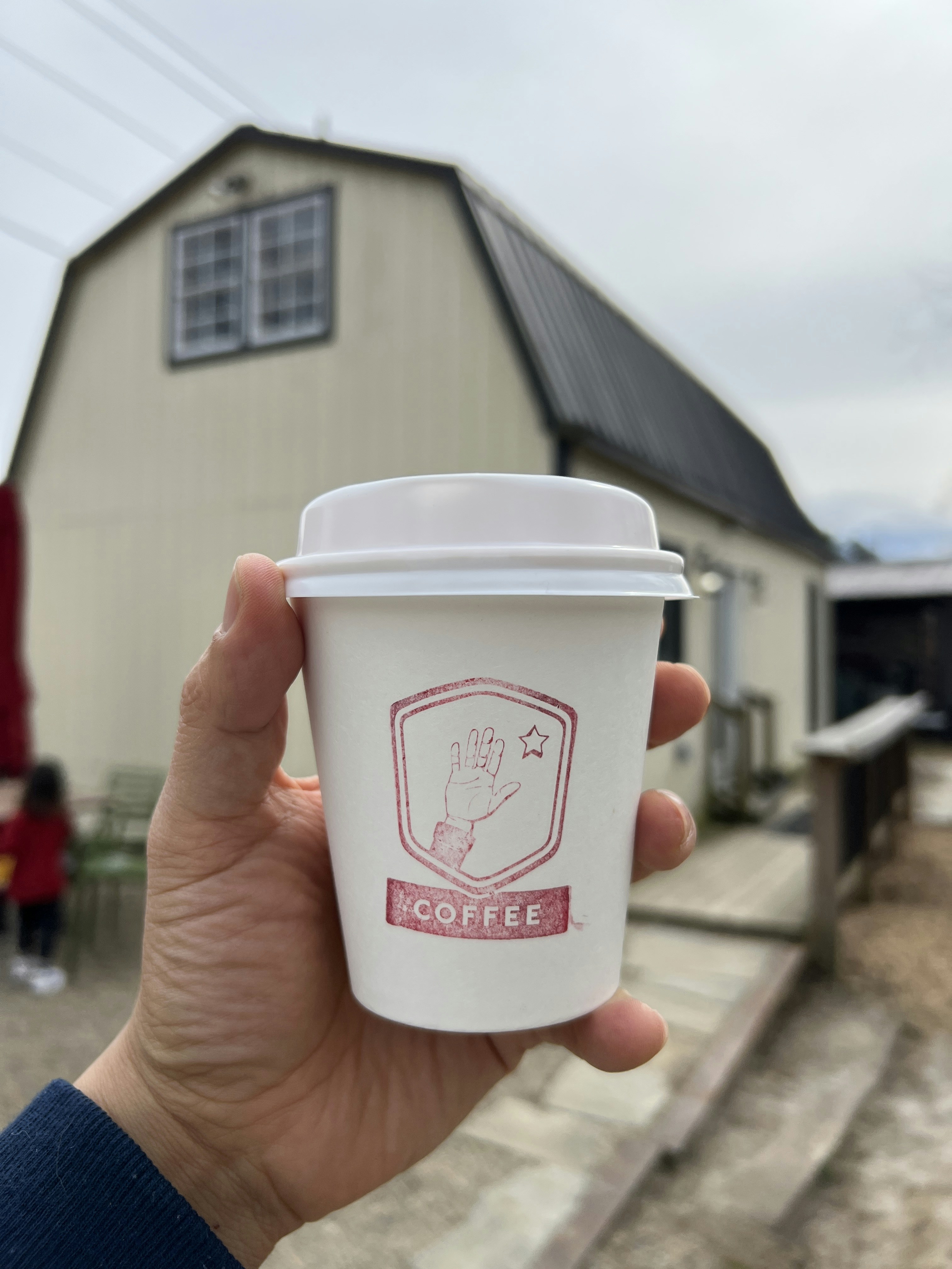 Cafe to Go: A Hand-Cupped Moment in Front of a Barn-Lined Street
