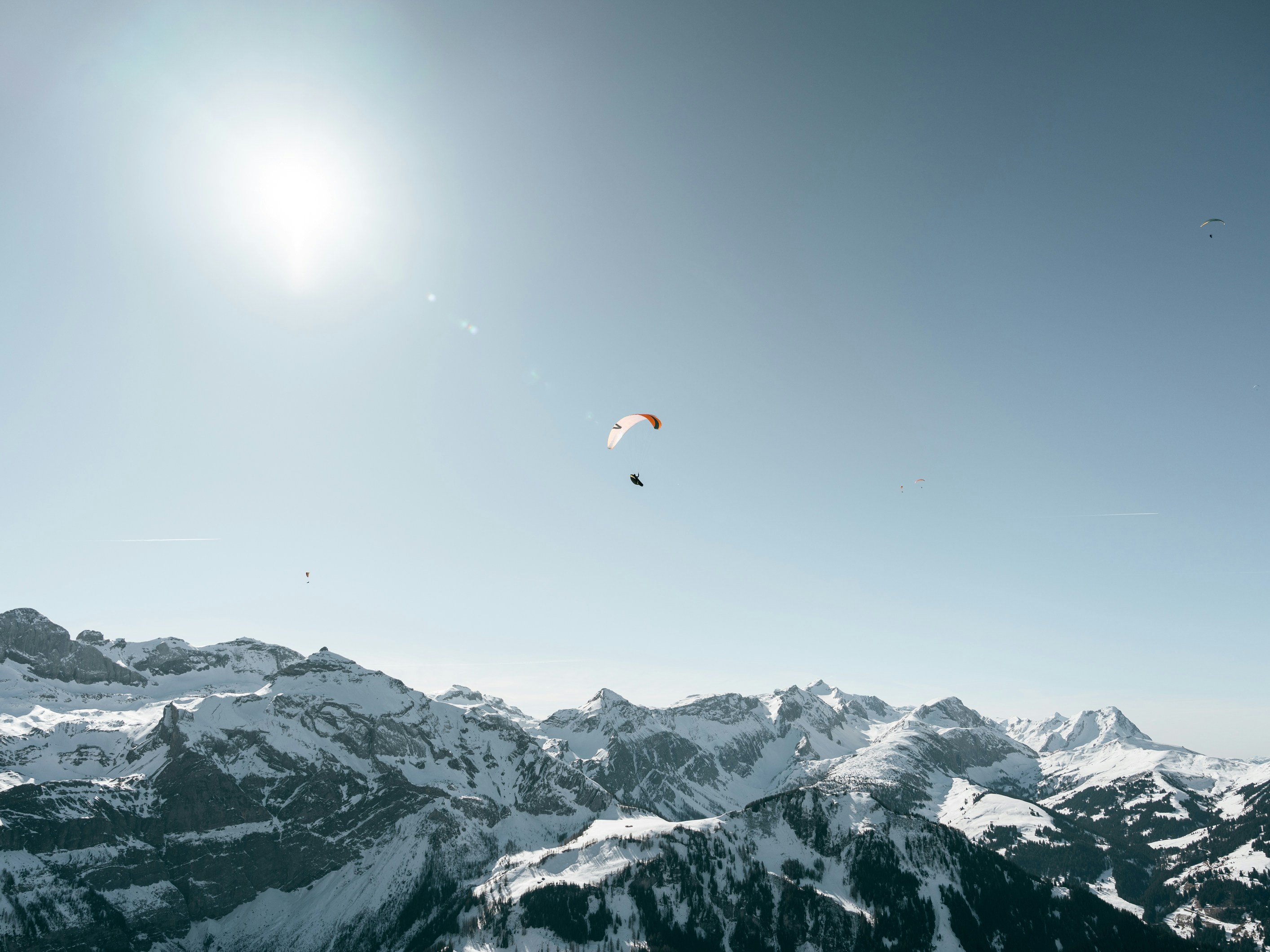 Paraglider Skims the Snowbound Crest Under a Clear Alpine Sky