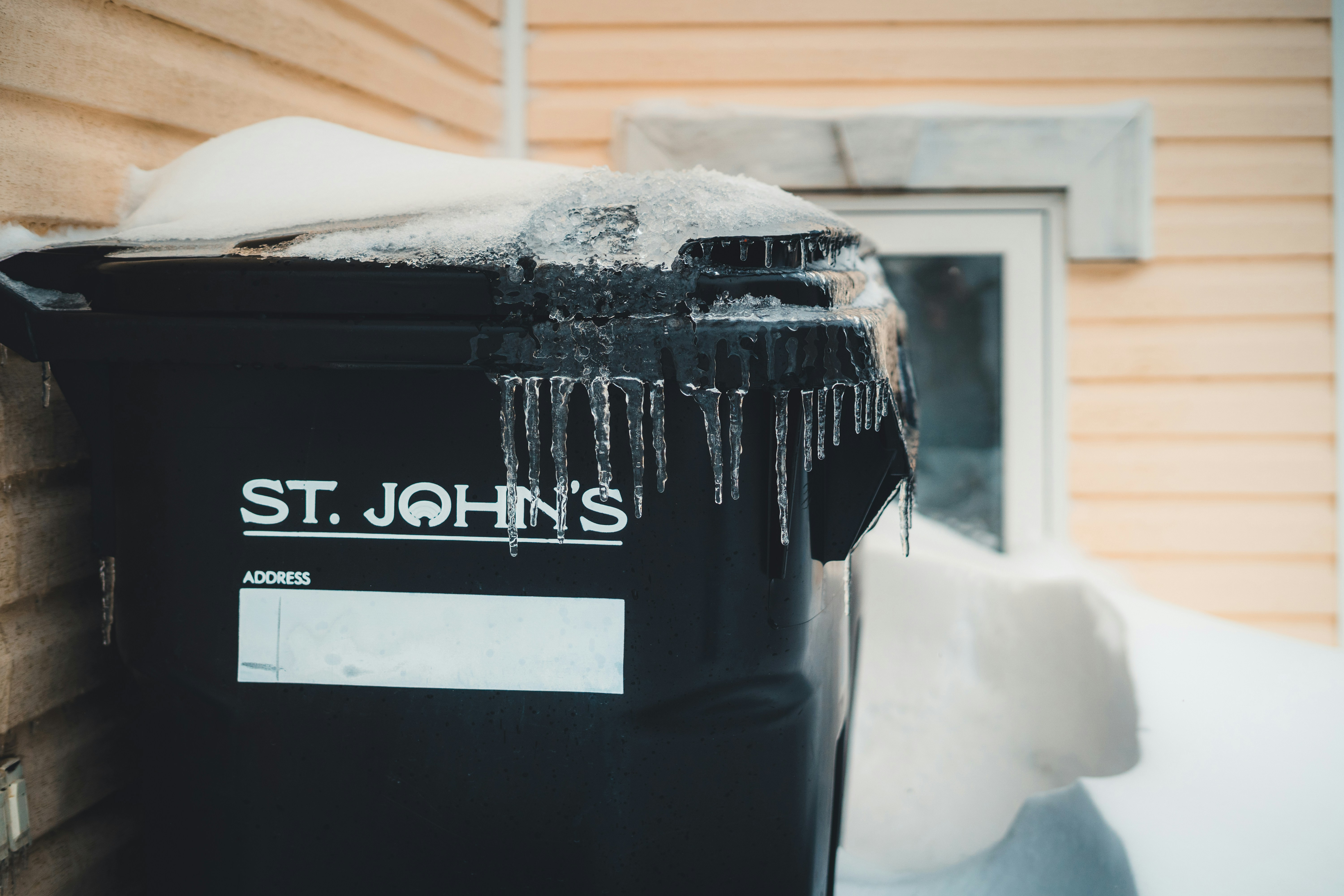 A black trash can covered in snow next to a building photo – Free Ice ...