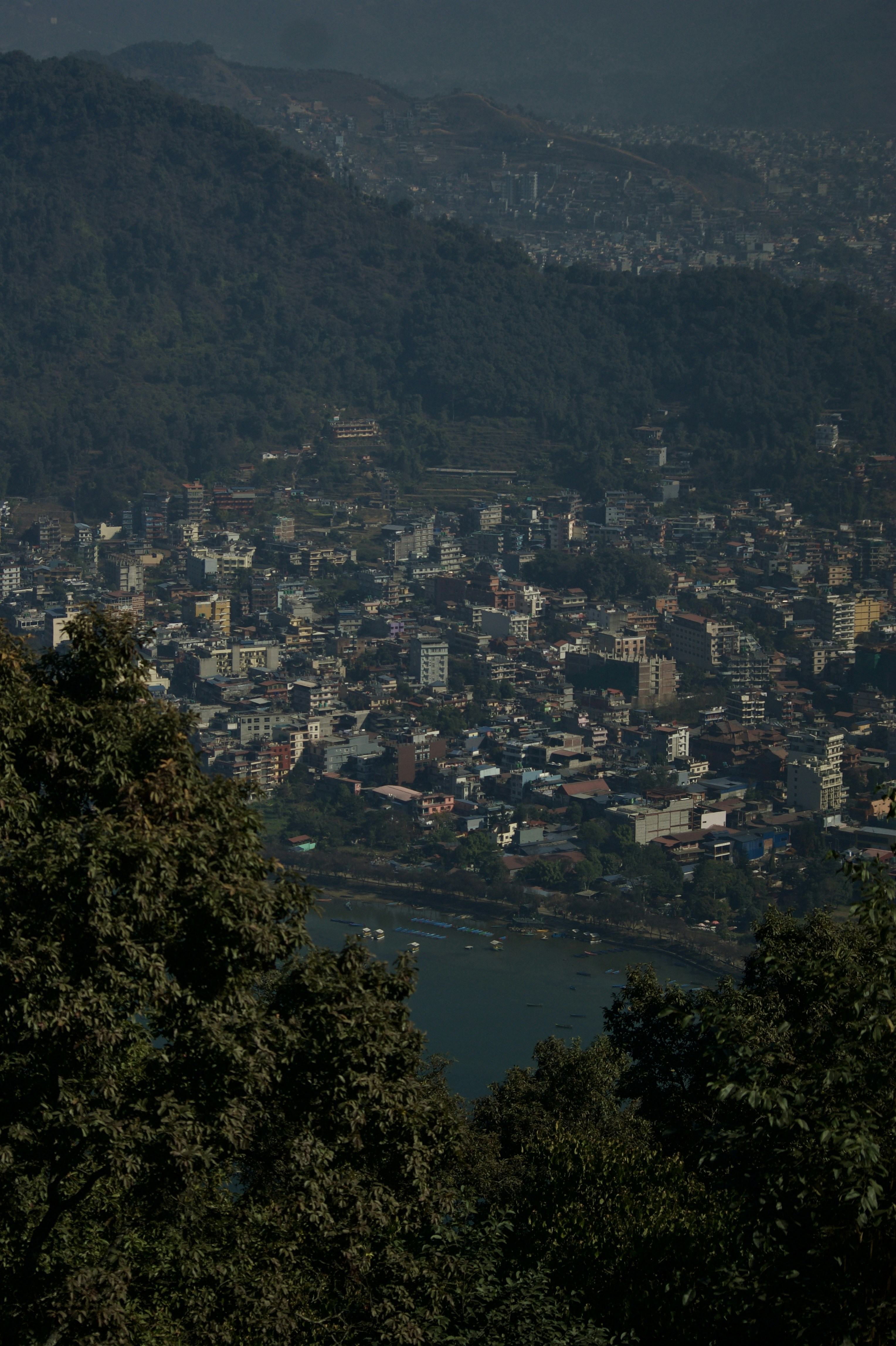 A panoramic view of a bustling cityscape framed by lush greenery and distant mountains. The scene captures the harmonious coexistence of urban life and natural surroundings.