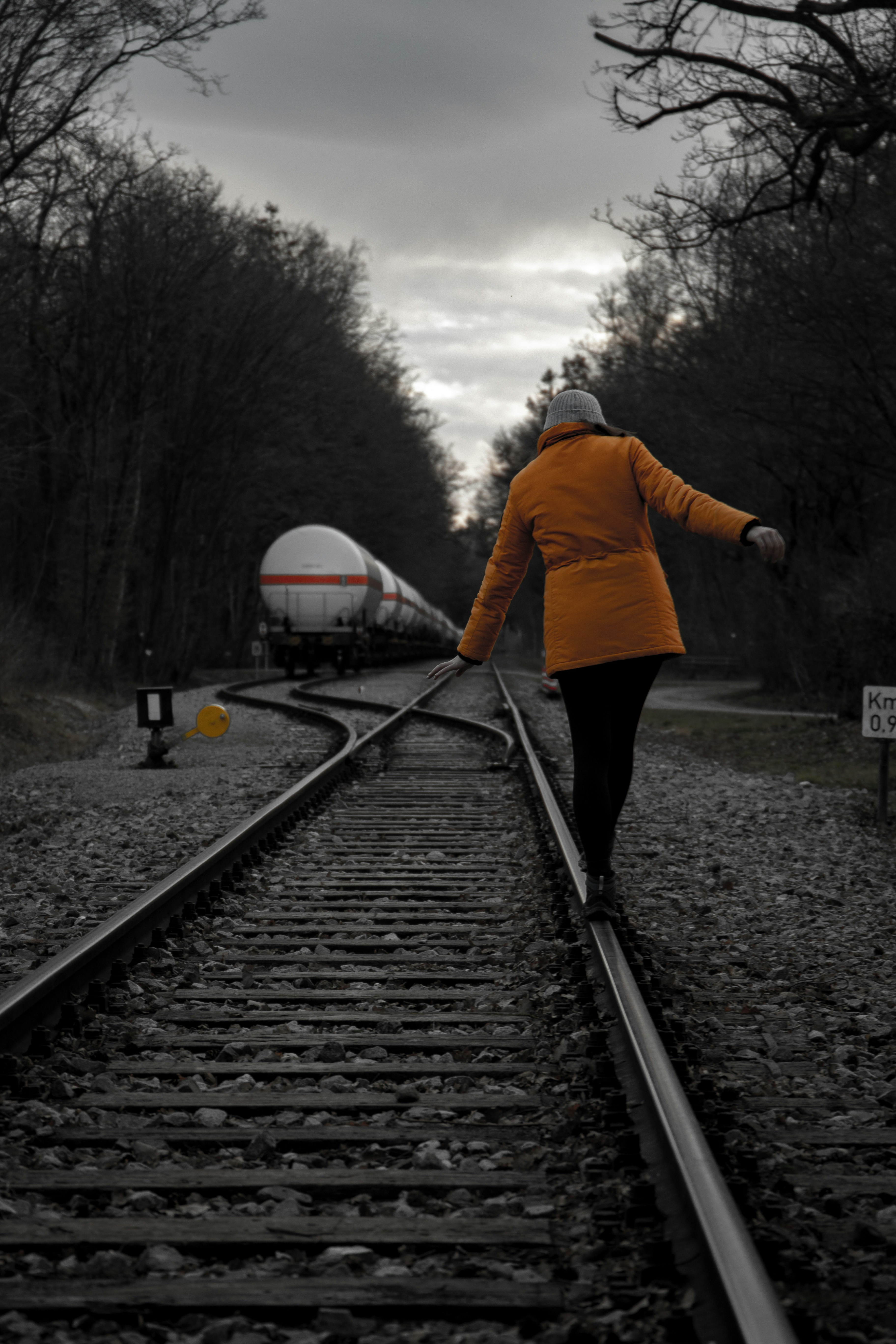 Balance on the Rails: A lone figure in an orange coat strides toward a distant tanker