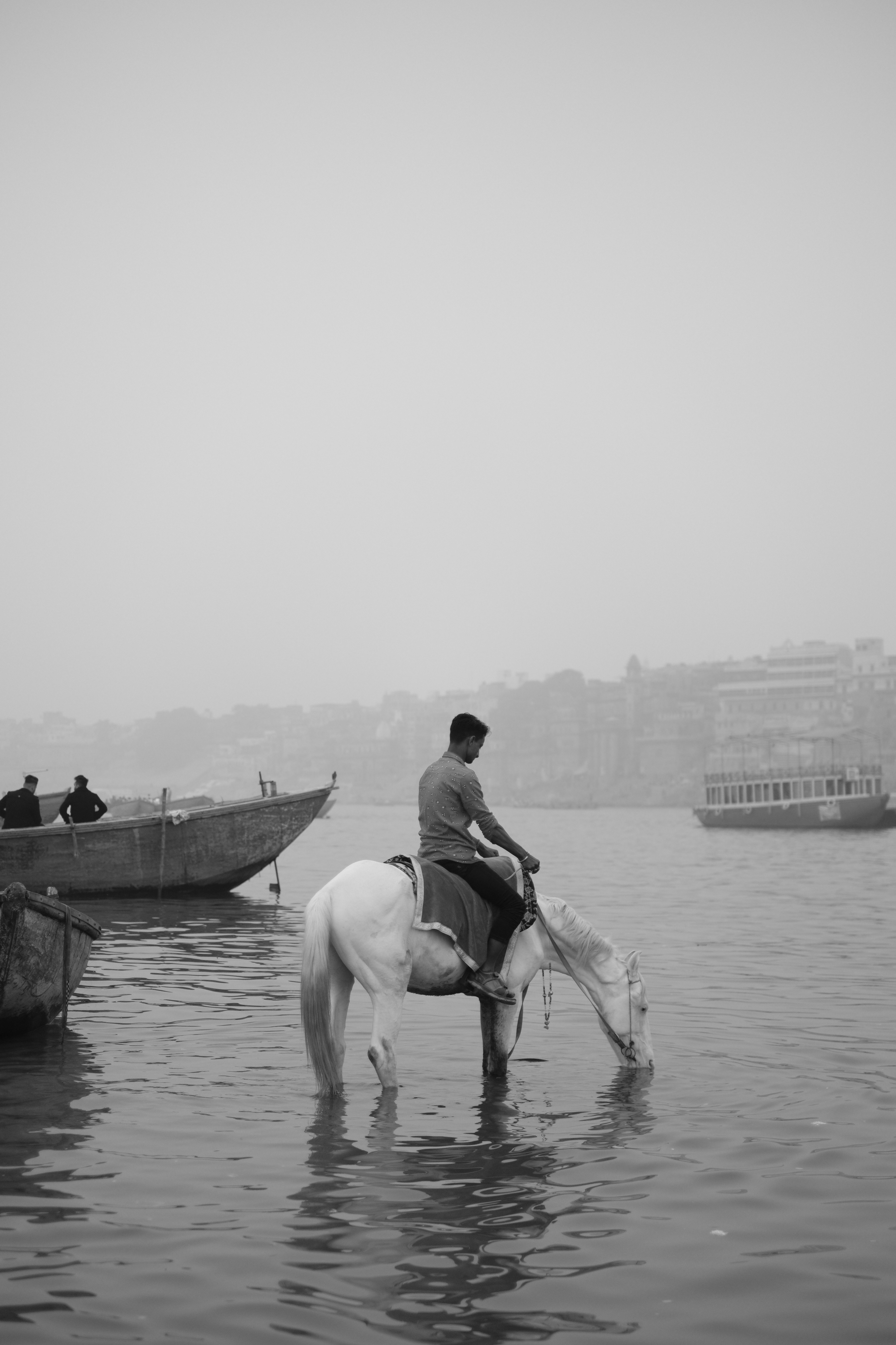 Quiet River Portrait: A Rider Steadying a White Horse Amid Fog and Boats