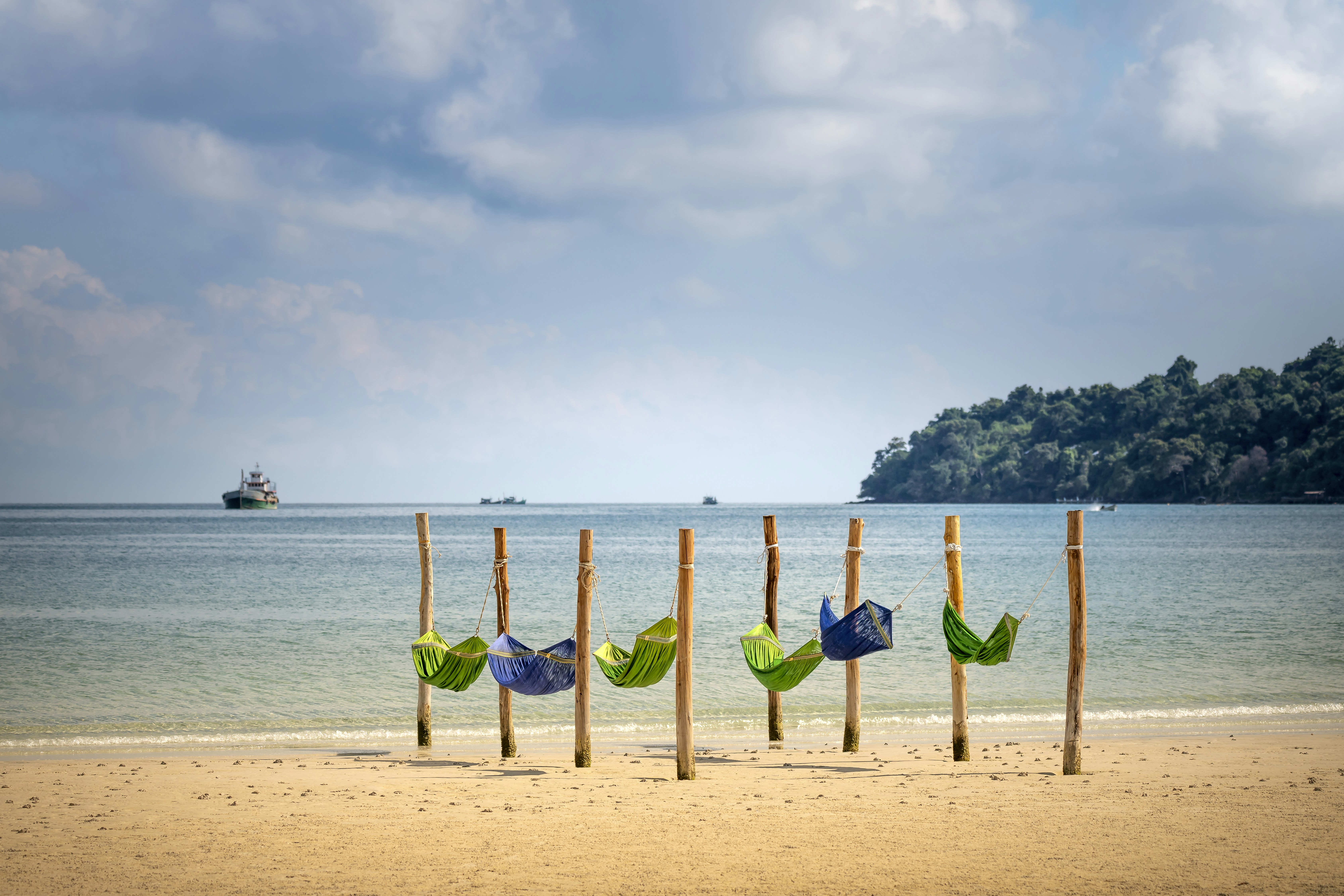 Colorful hammocks anchored by wooden poles on a tranquil tropical shore