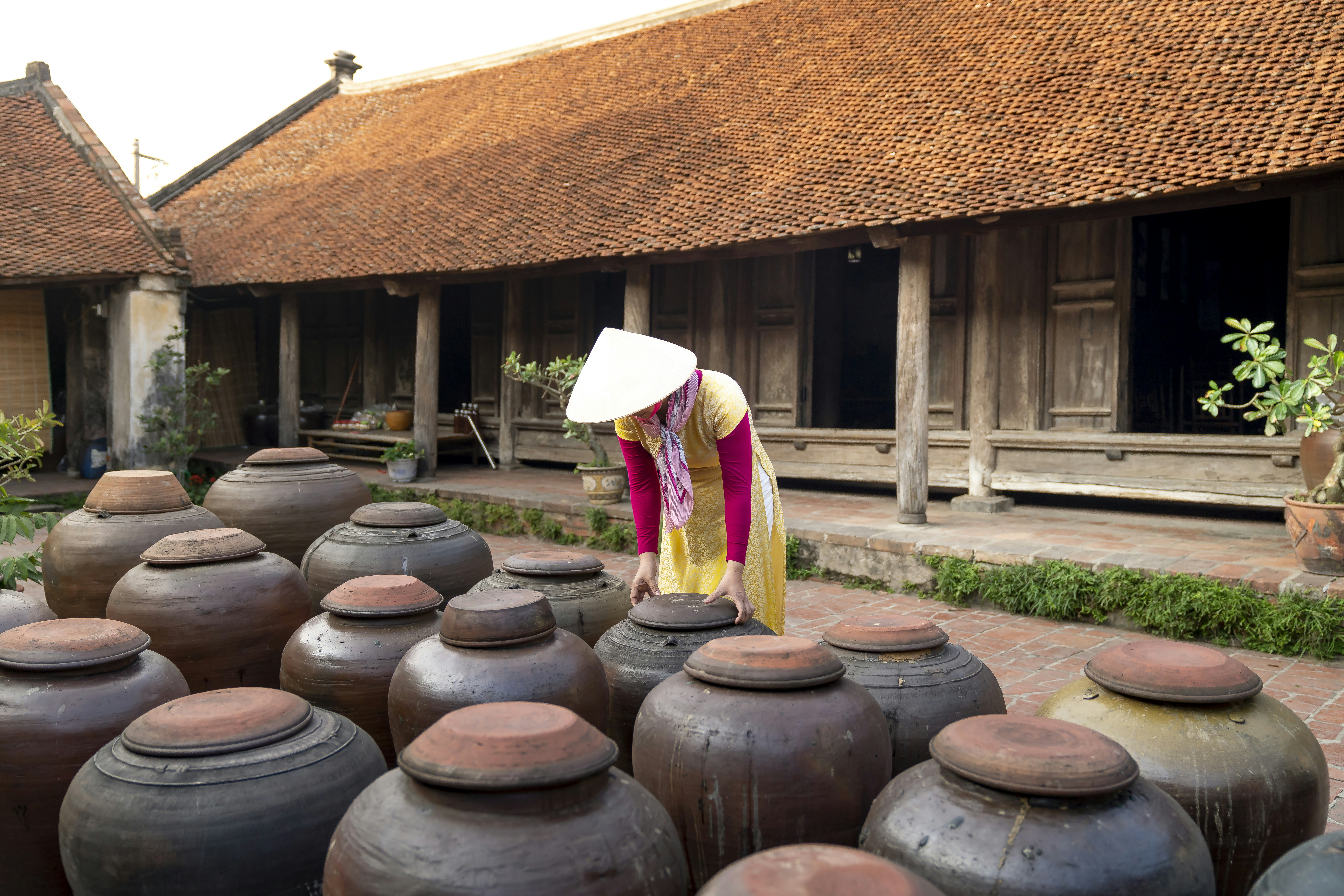 Conical-Hat Figure Among Thousands of Clay Jars in a Sunlit Courtyard