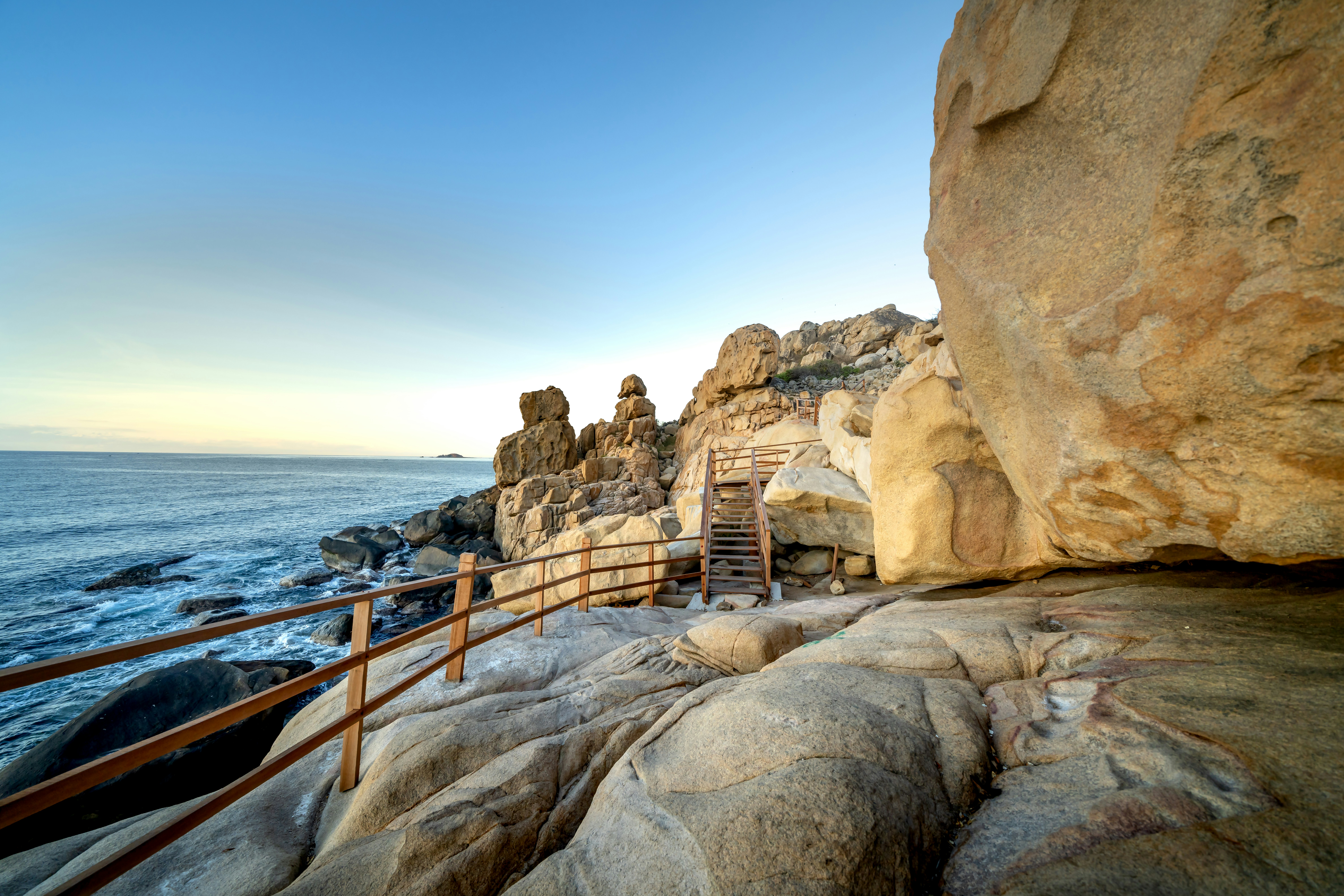 A rocky cliff next to the ocean with stairs leading to it photo – Free ...