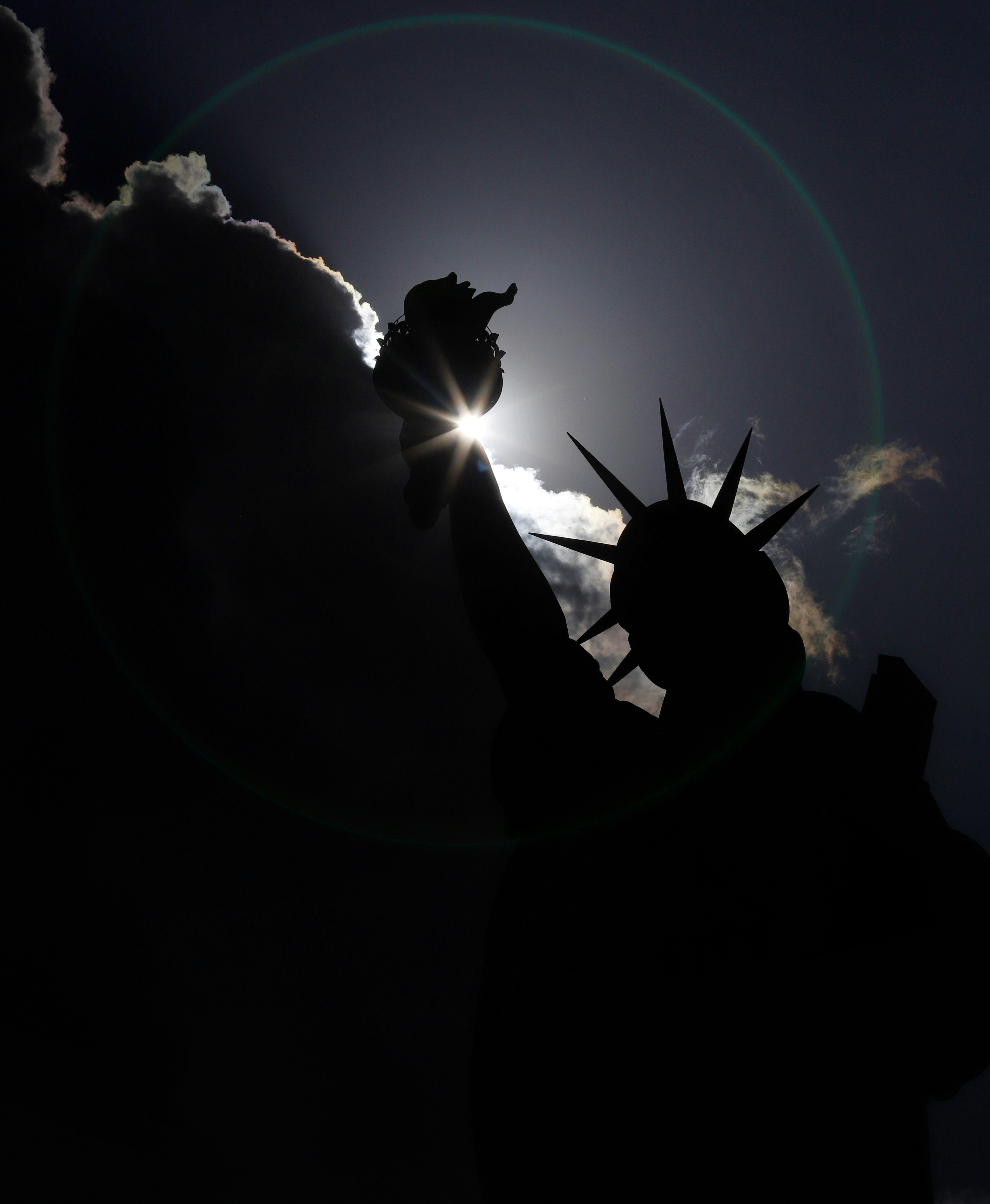 Haloed Liberty: A Backlit Torch Silhouette Against a Radiant Sky