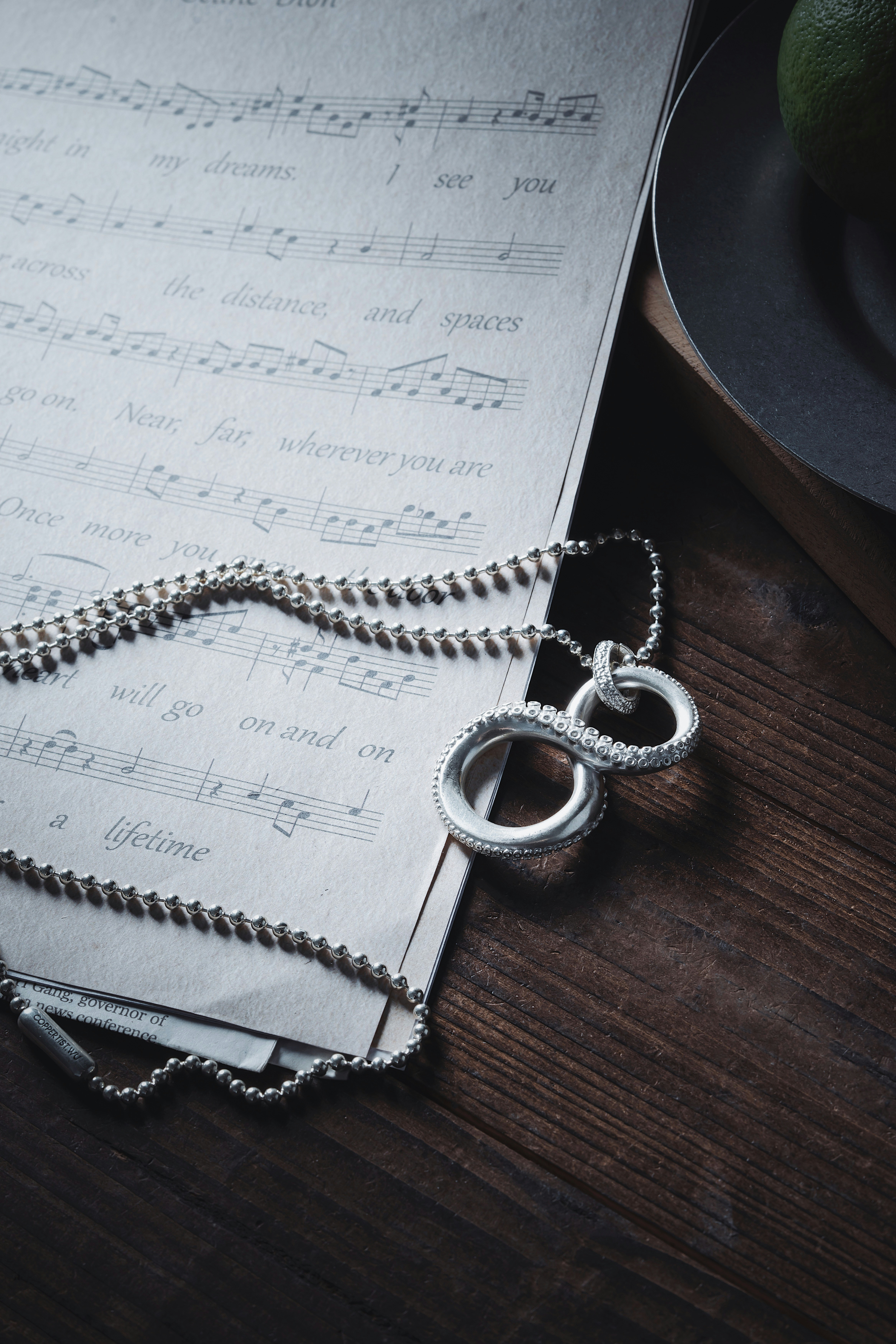 Double-Ring Pendant Draped Across Sheet Music on a Dark Wooden Desk
