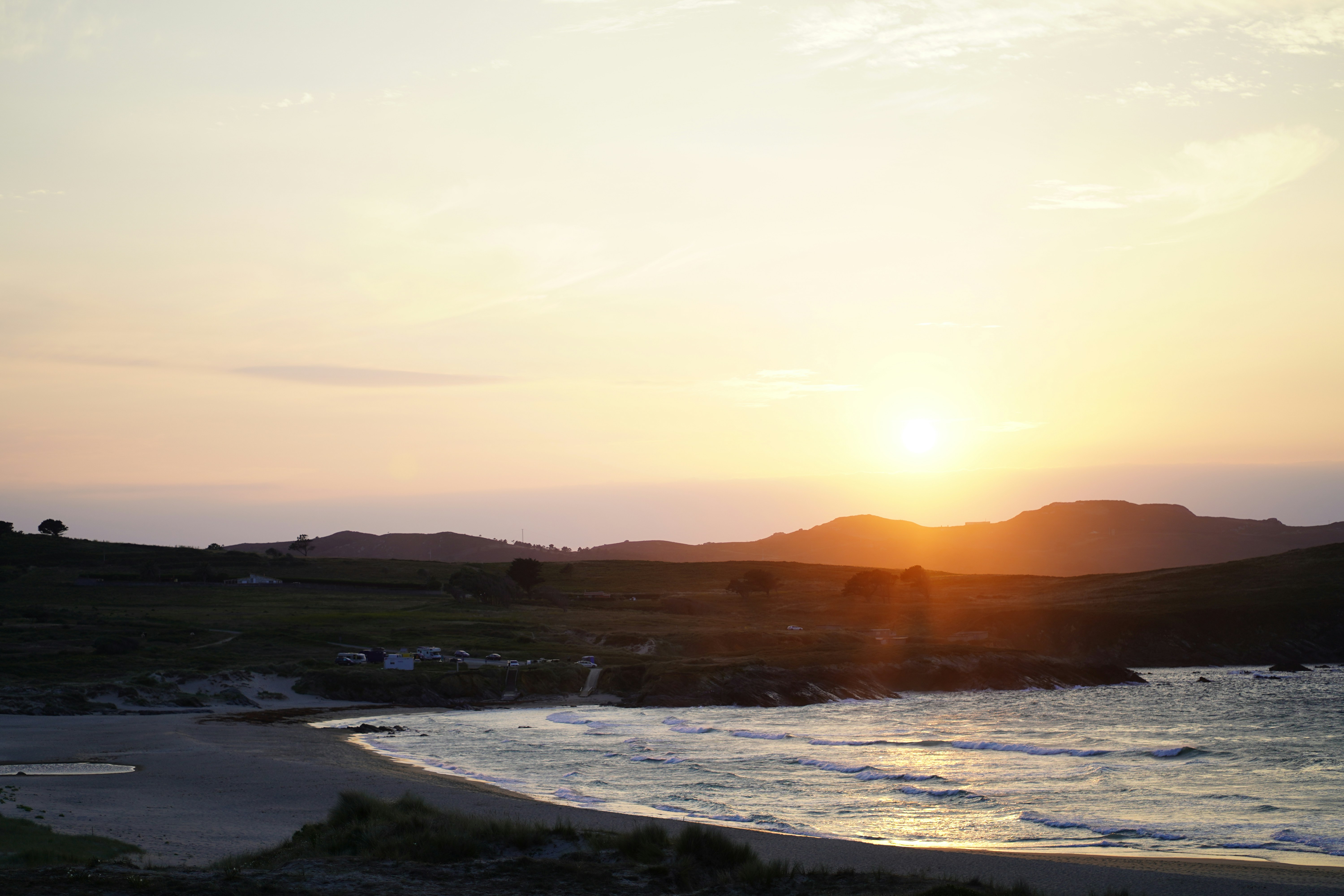 Sunset casting warm hues over rolling hills and a tranquil coastline.