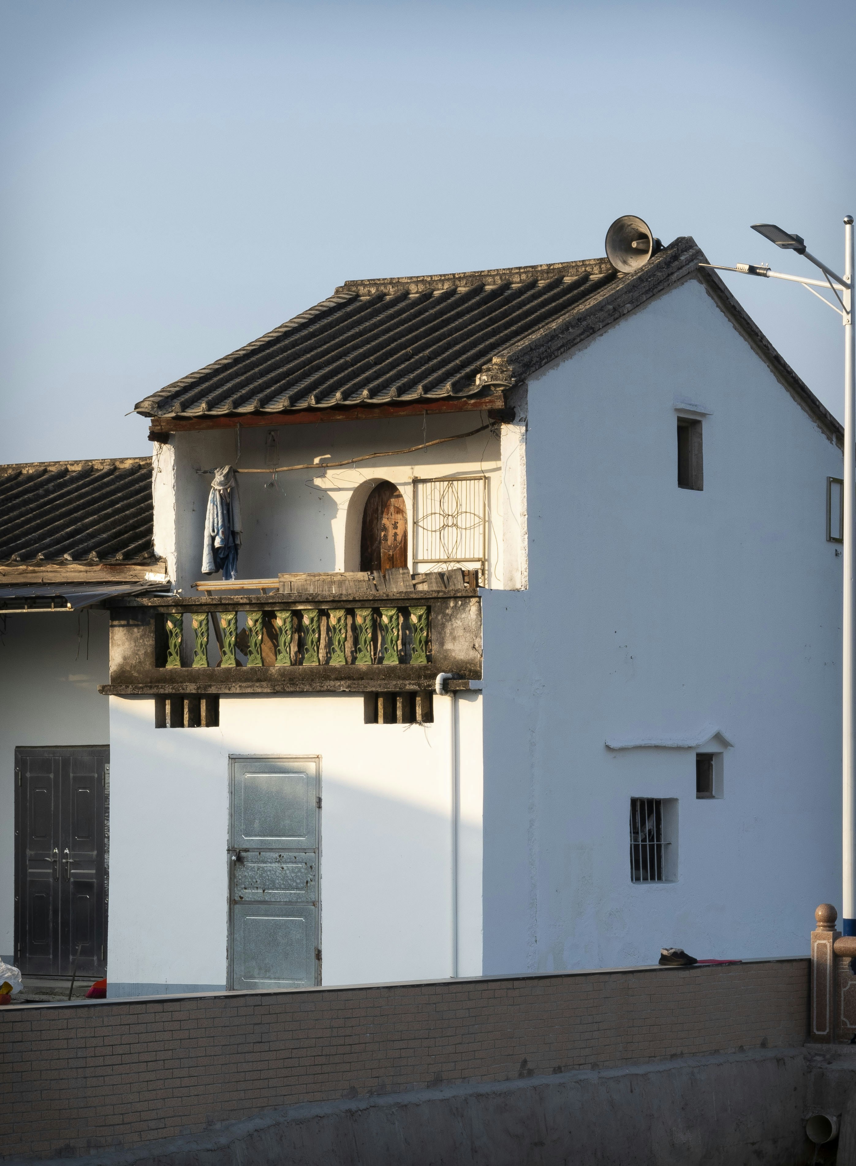 Arched Balcony Portrait: Sunlit White-Walled House with Weathered Wood Railings
